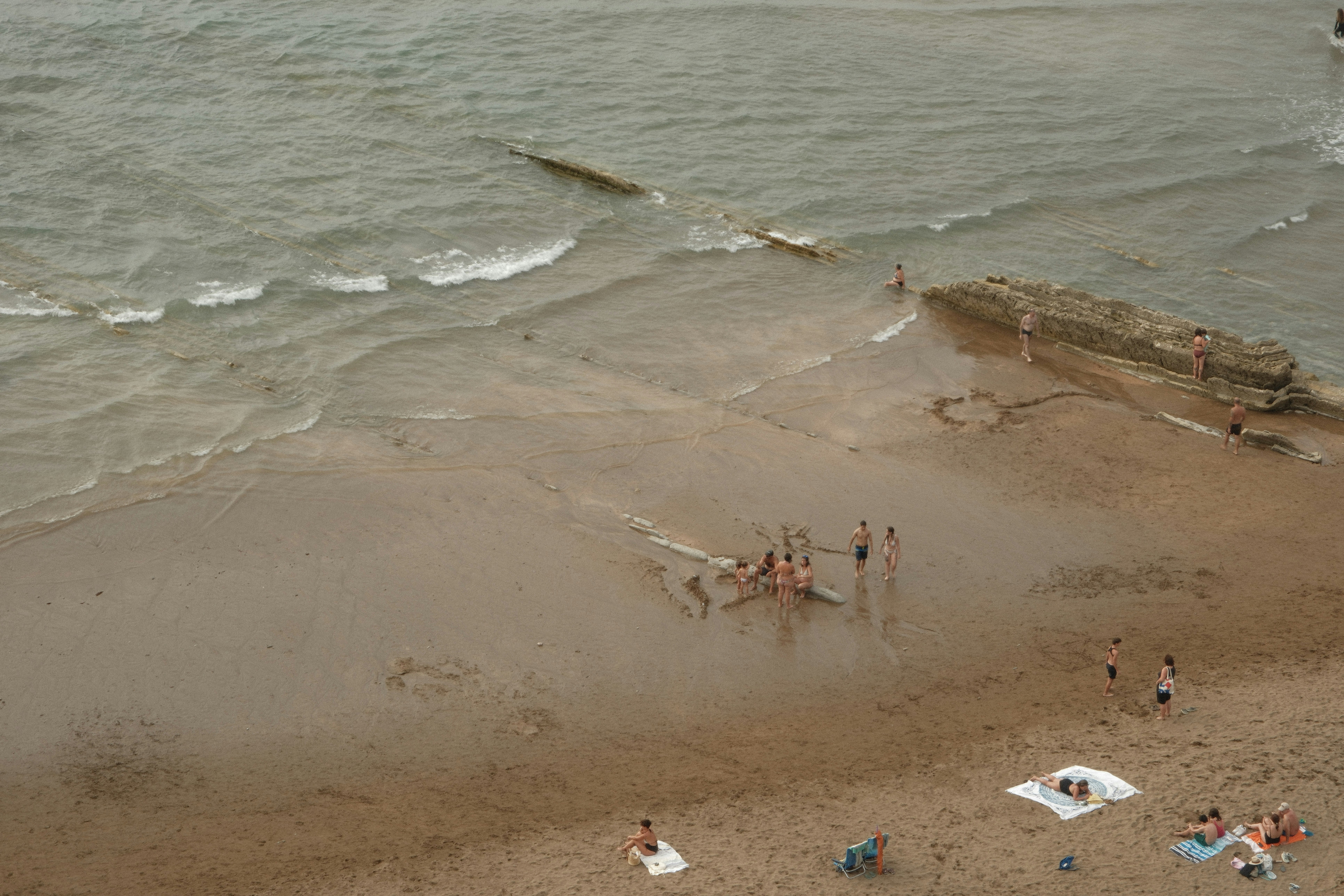 Sunlit Shoreline: Aerial Perspective of Beachgoers and Tidal Rocks
