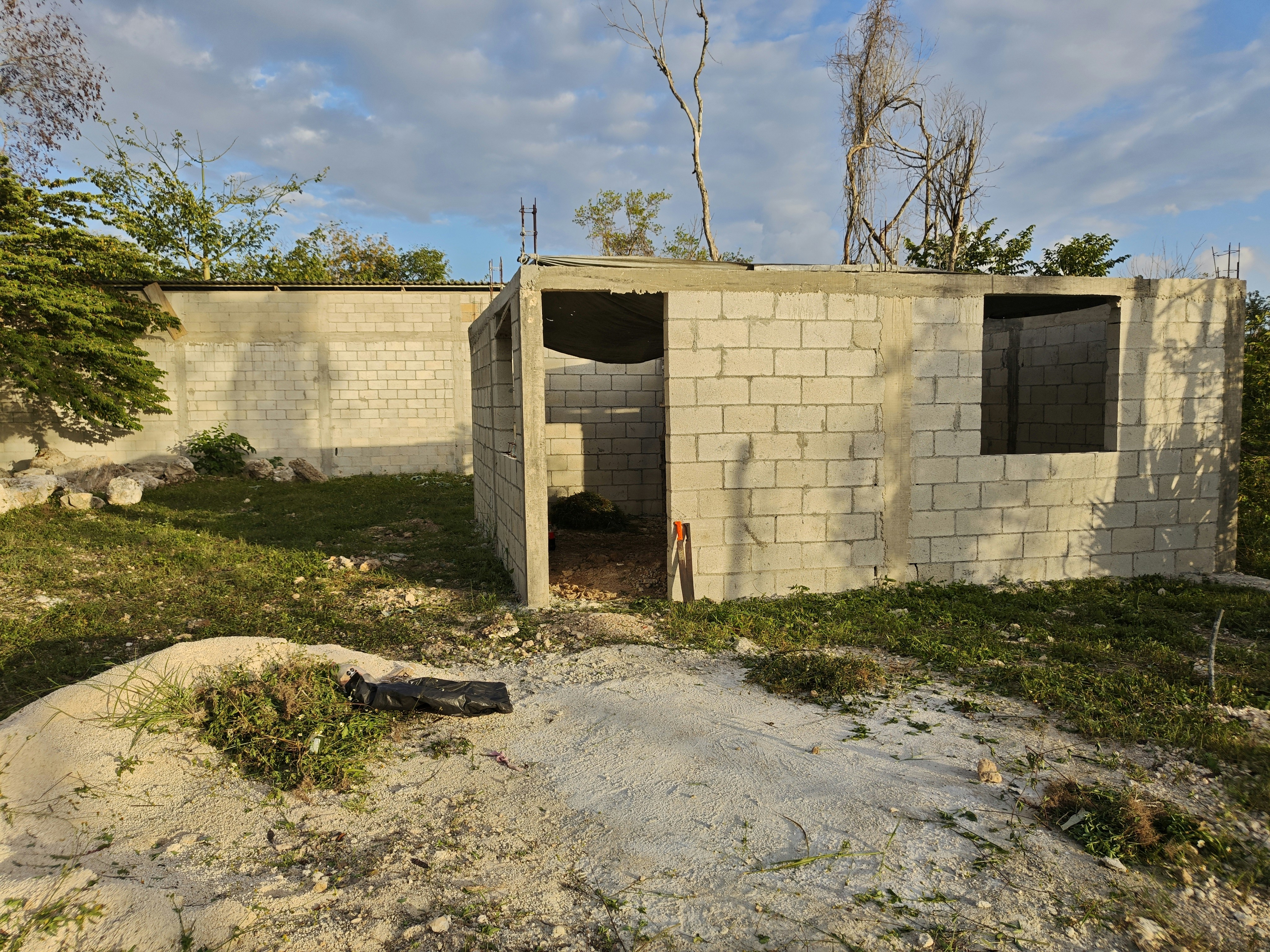 An unfinished concrete block structure in a grassy yard under a blue sky.