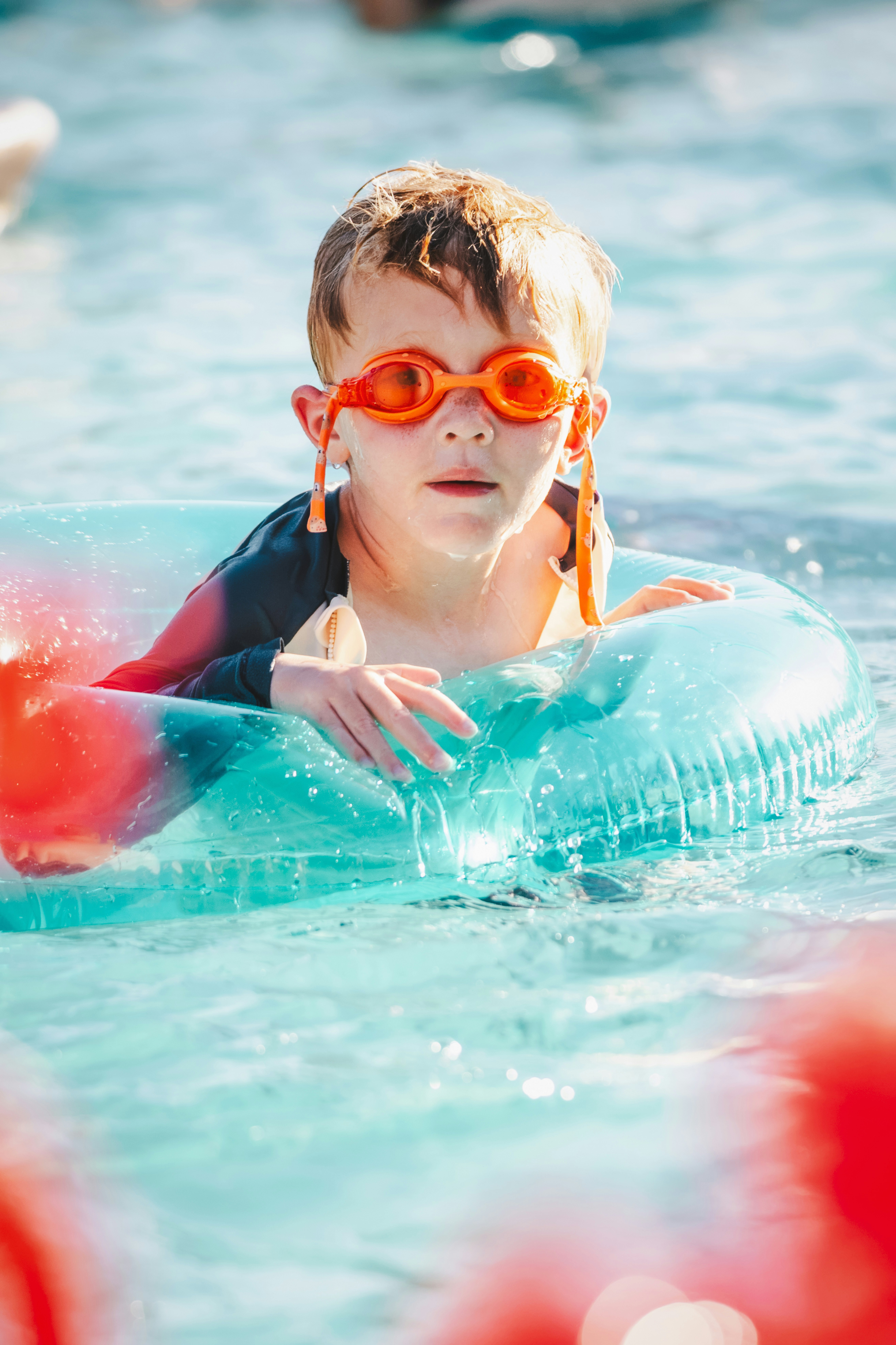 Sunlit Swim: Child in Bright Orange Goggles Floats in Aqua Ring