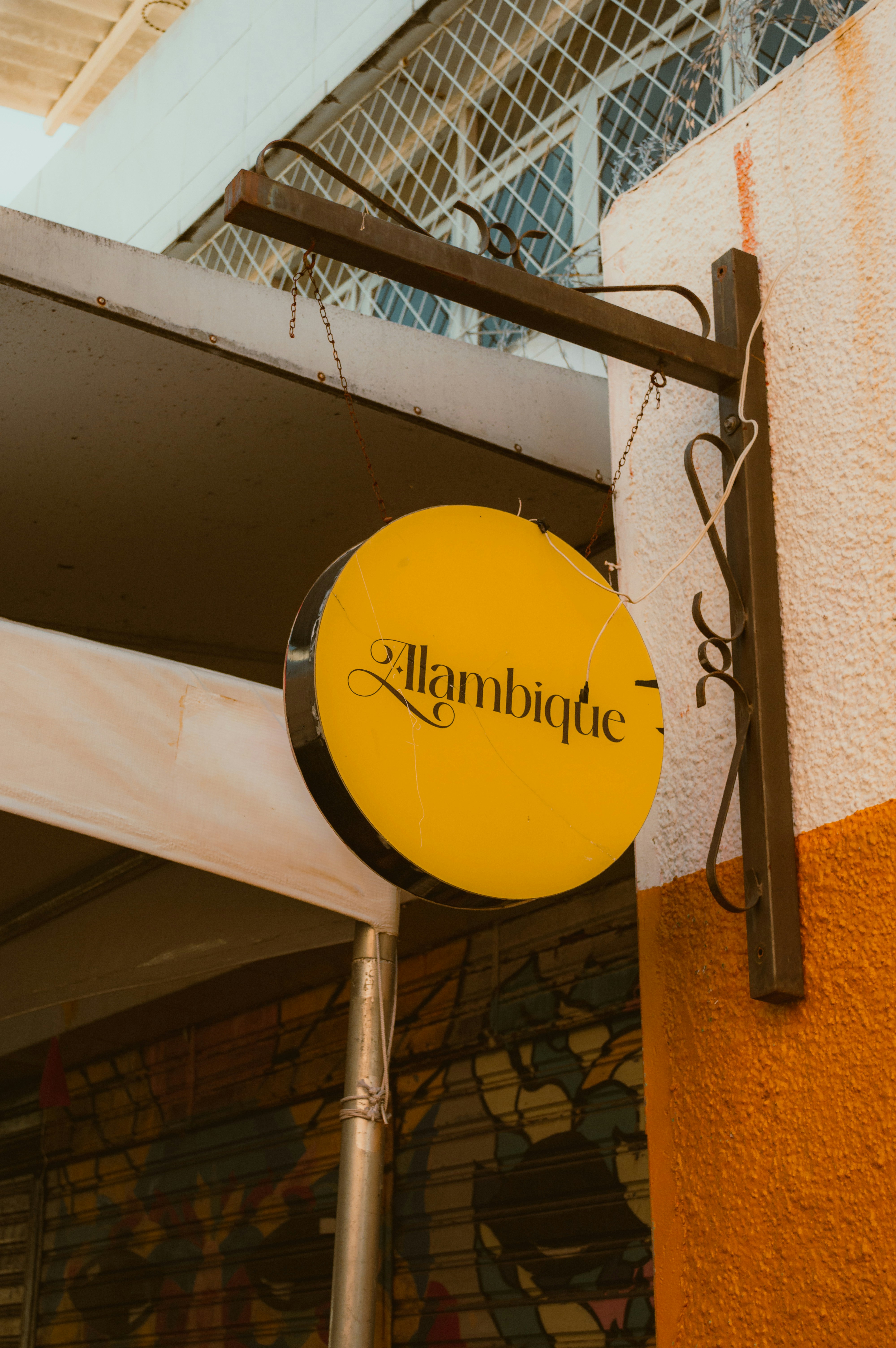 Yellow round sign of Allambique on a storefront under muted urban shade