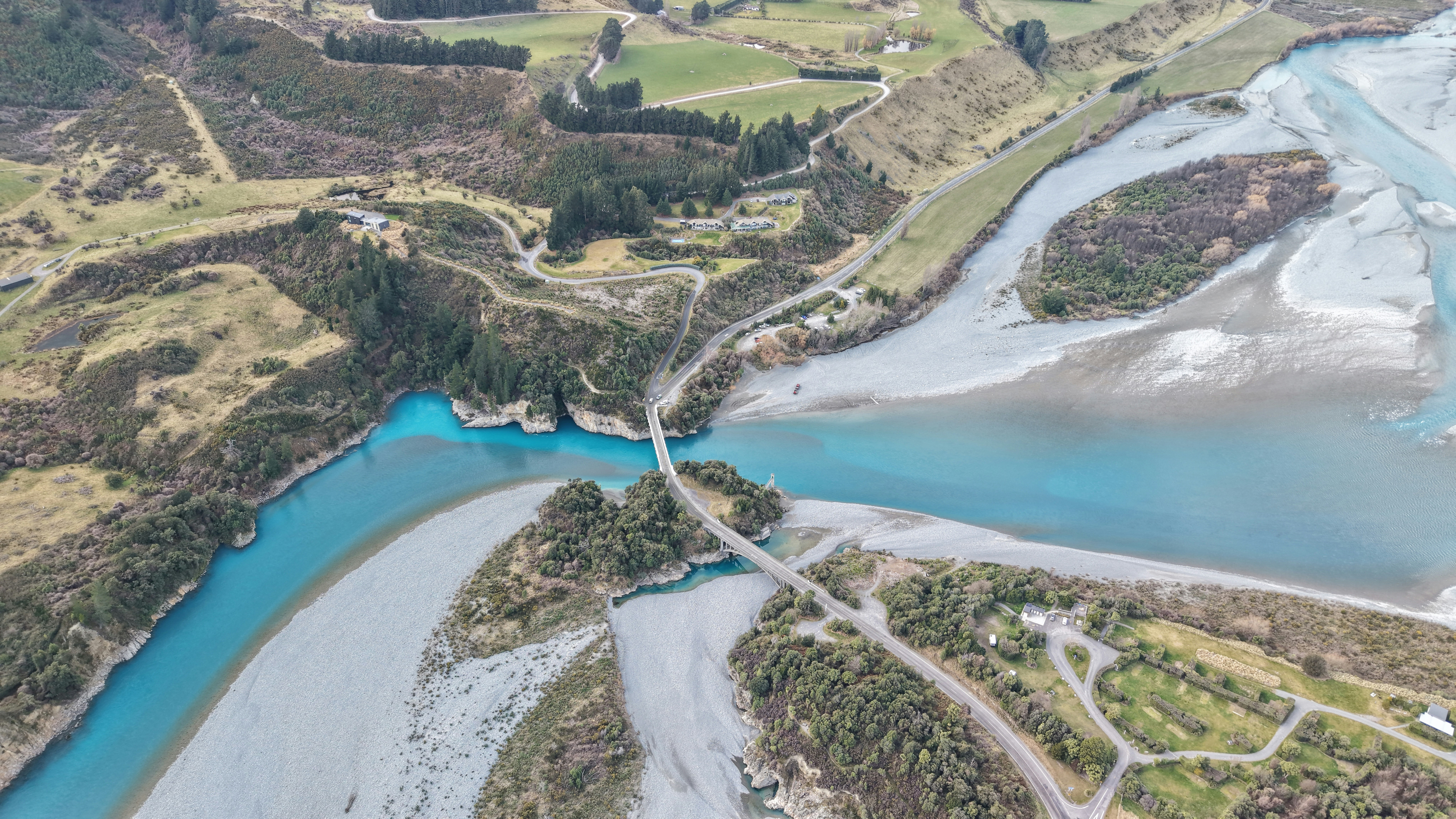 An aerial view of a bridge crossing a bright blue river in a valley.
