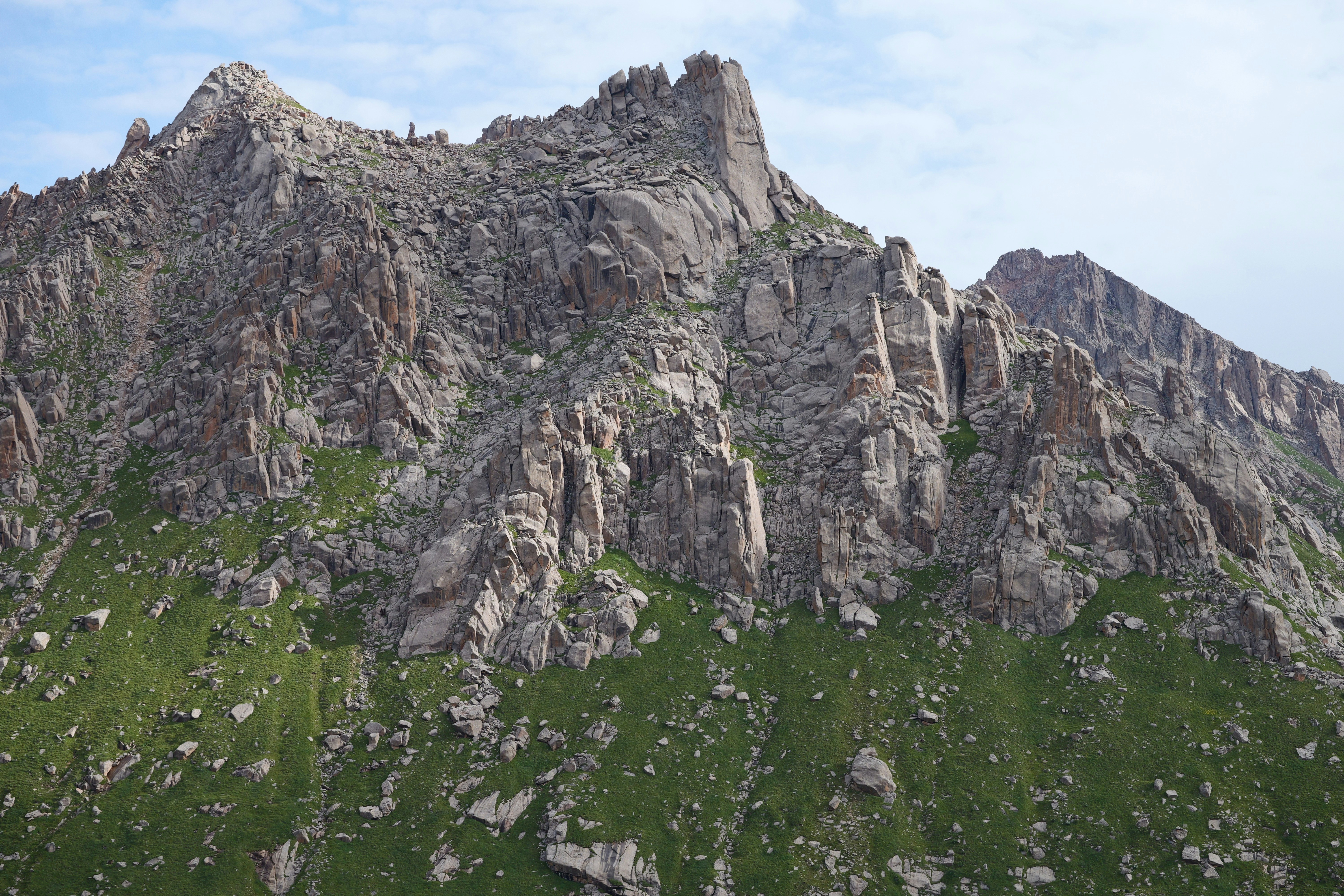 Jagged Summit: Sunlit Granite Against a Green Slope