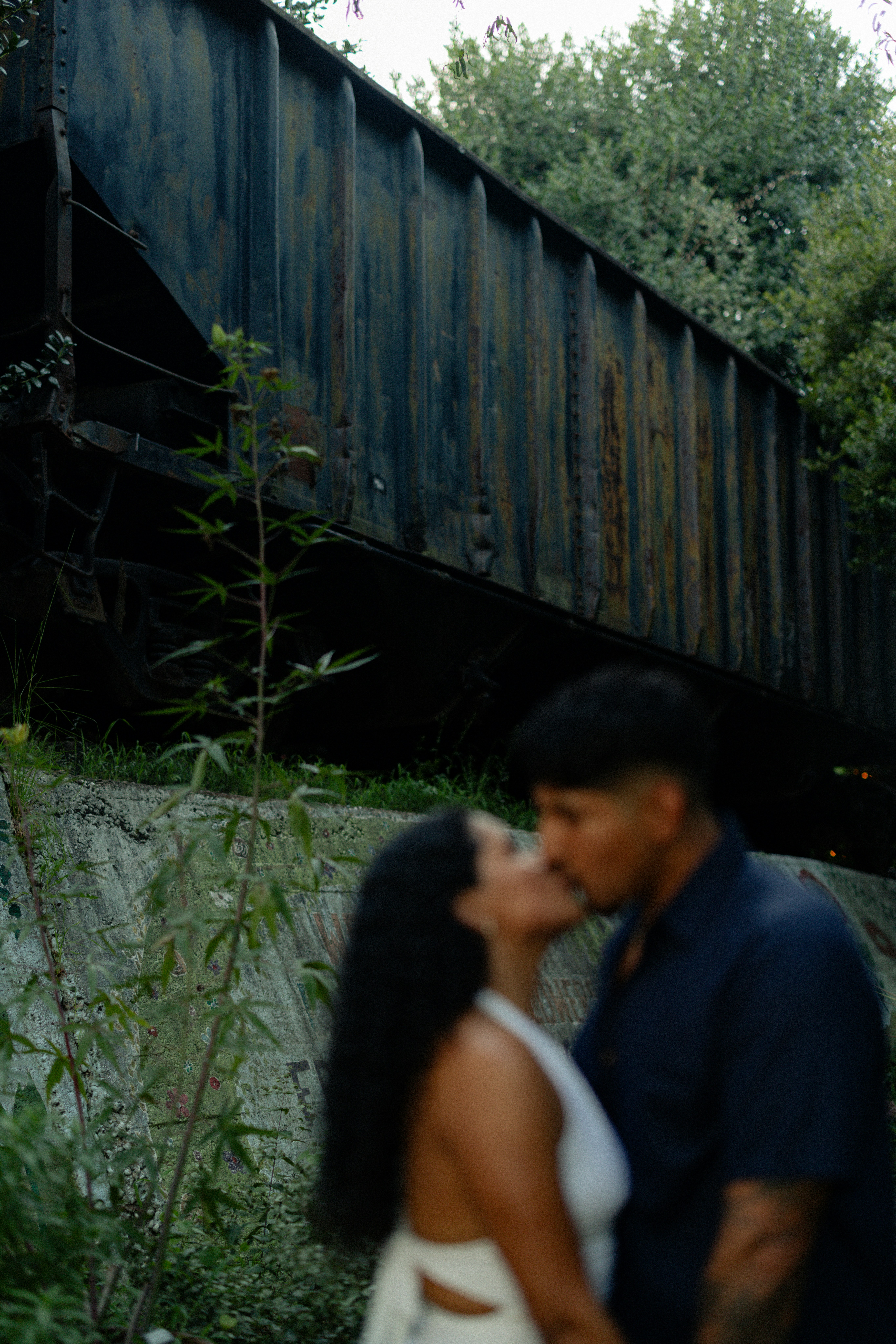 Kiss by the Tracks: A Quiet Moment Under a Rusted Bridge