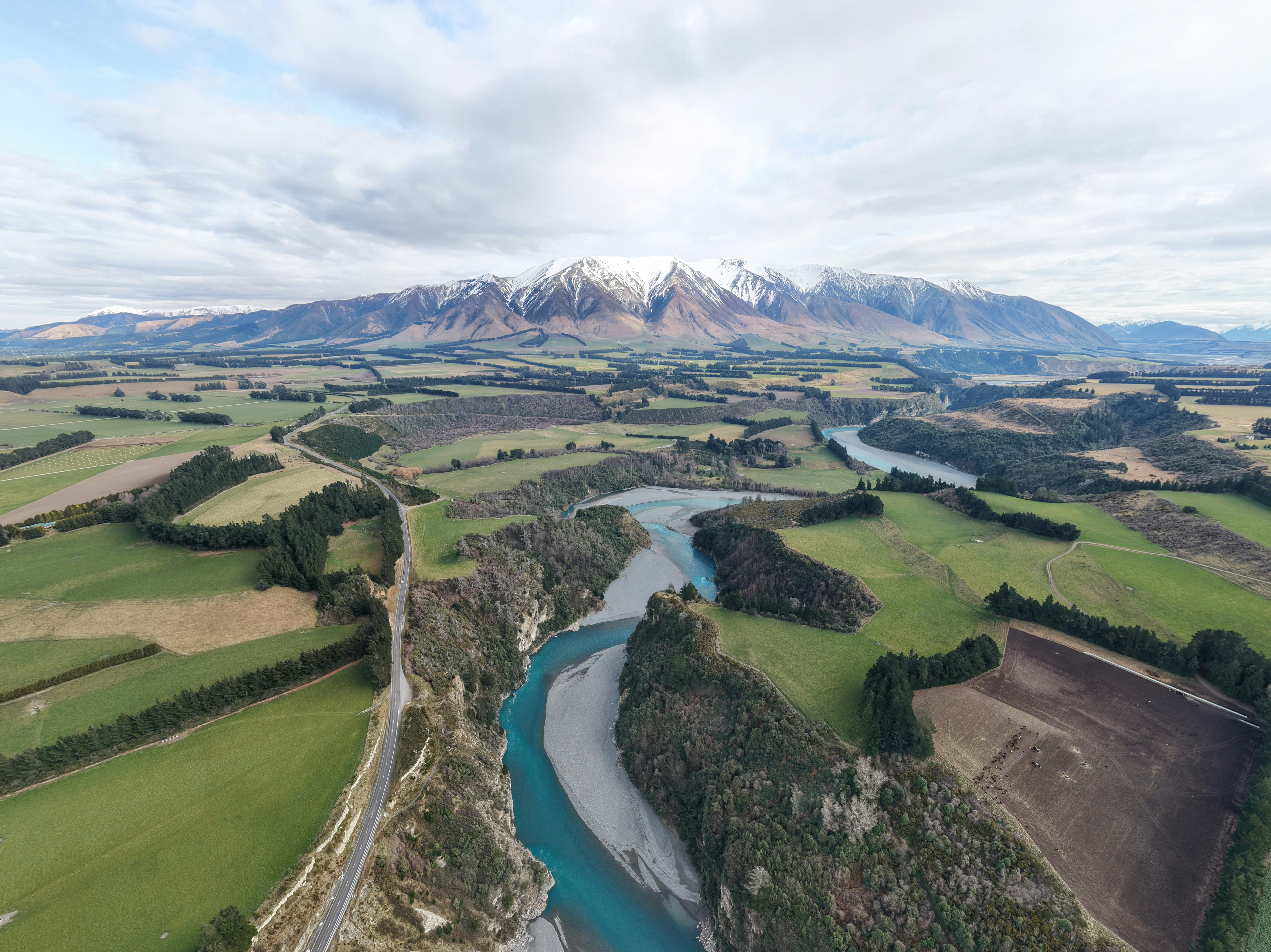 Aerial Confluence: River Valleys Carve Through Verdant Fields Beneath Snow-Kissed Peaks