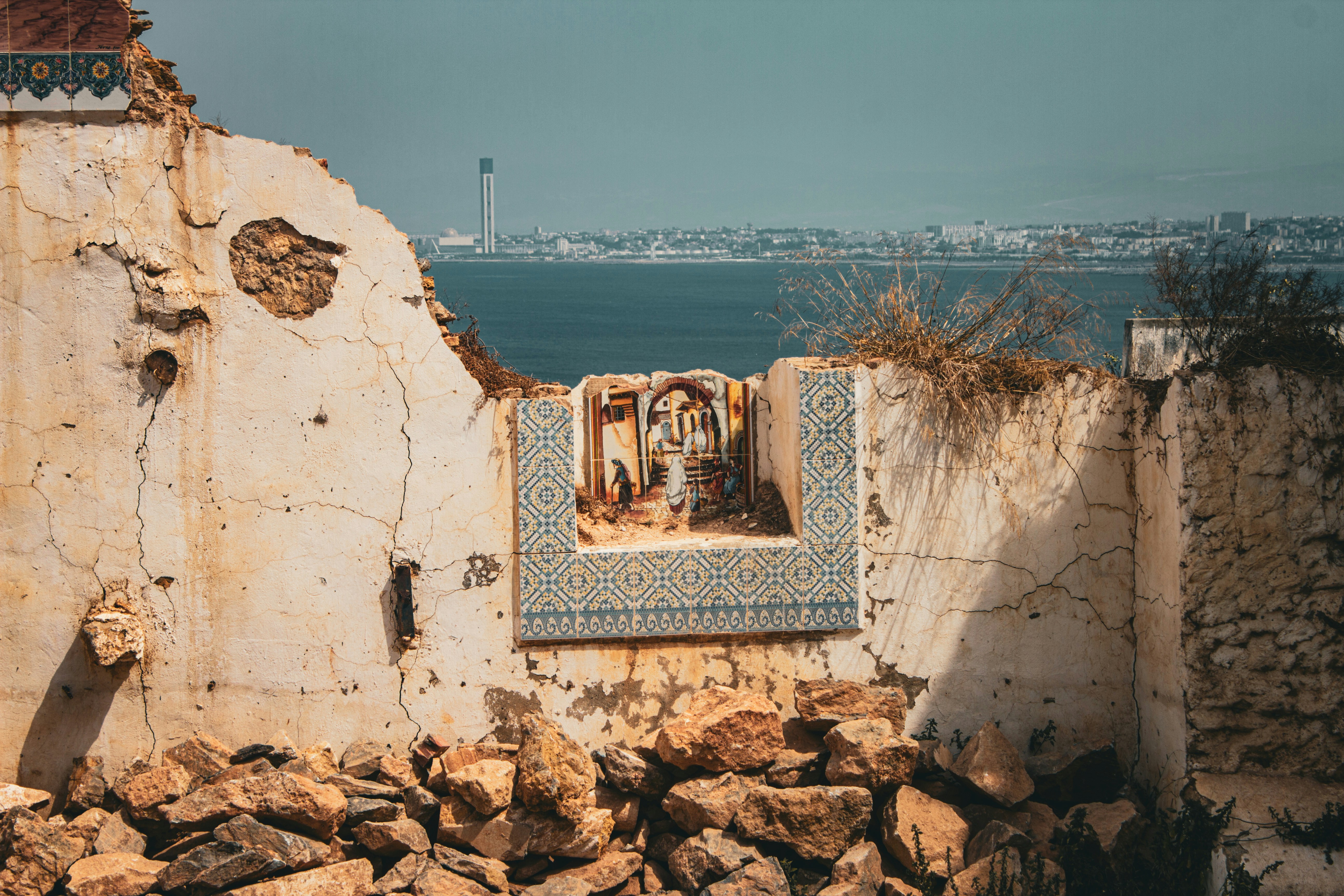 Tile-framed doorway in sunlit coastal ruin gazing toward distant city