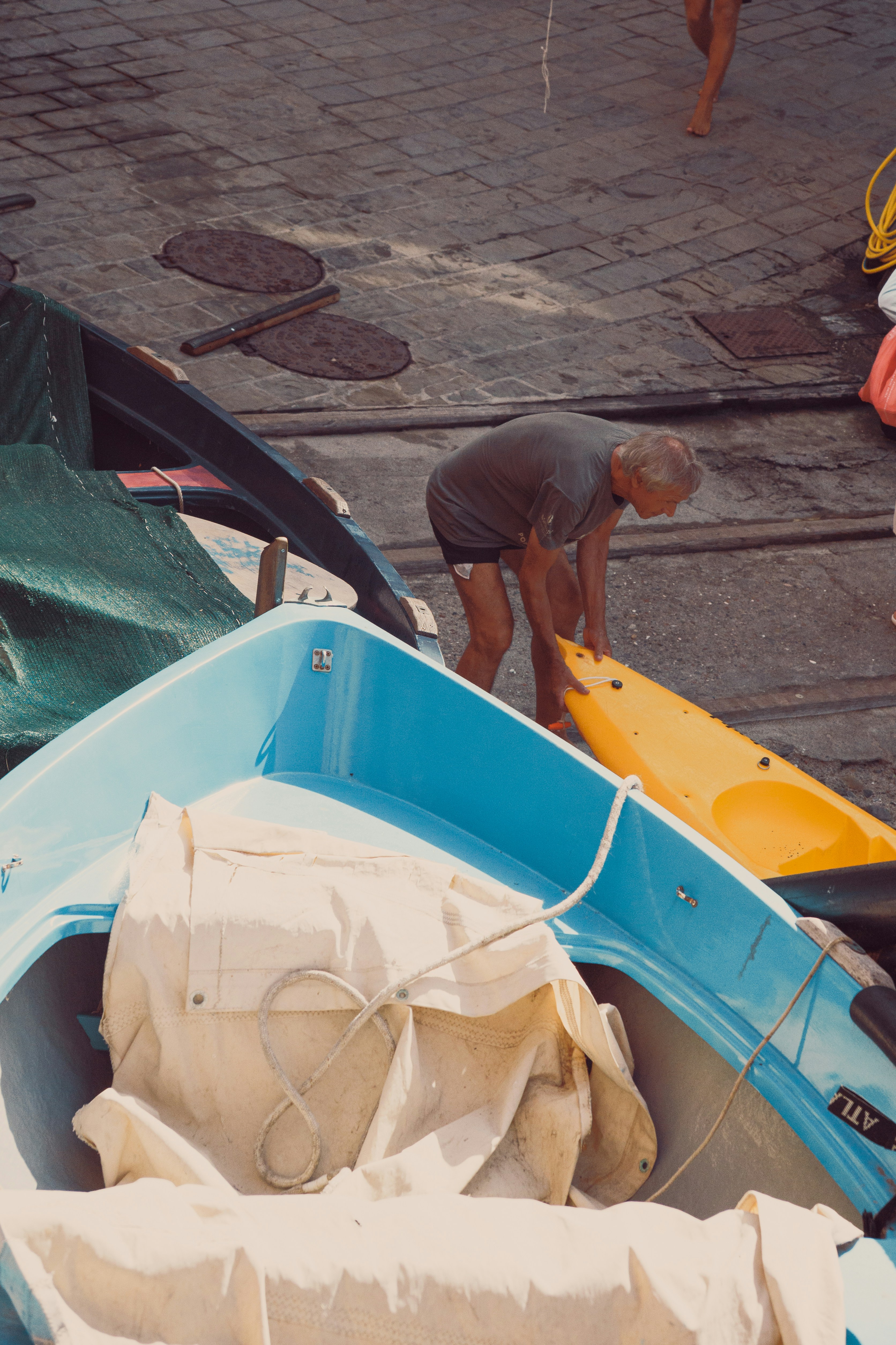 Dockside Tug: An Elderly Worker Aligns the Yellow Kayak Beside a Bright Boat