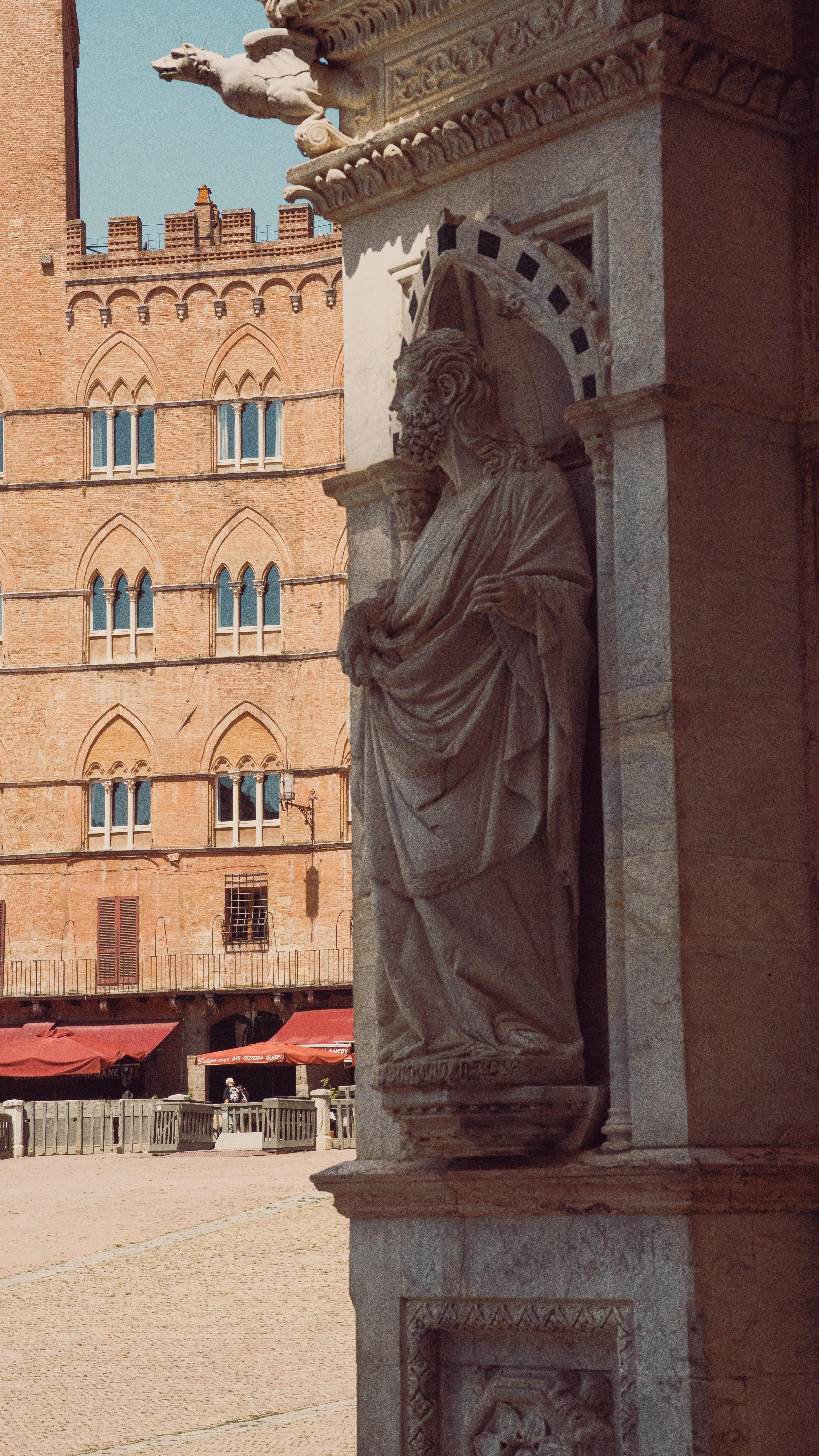 Statue of a robed figure at the archway of a brick historic square