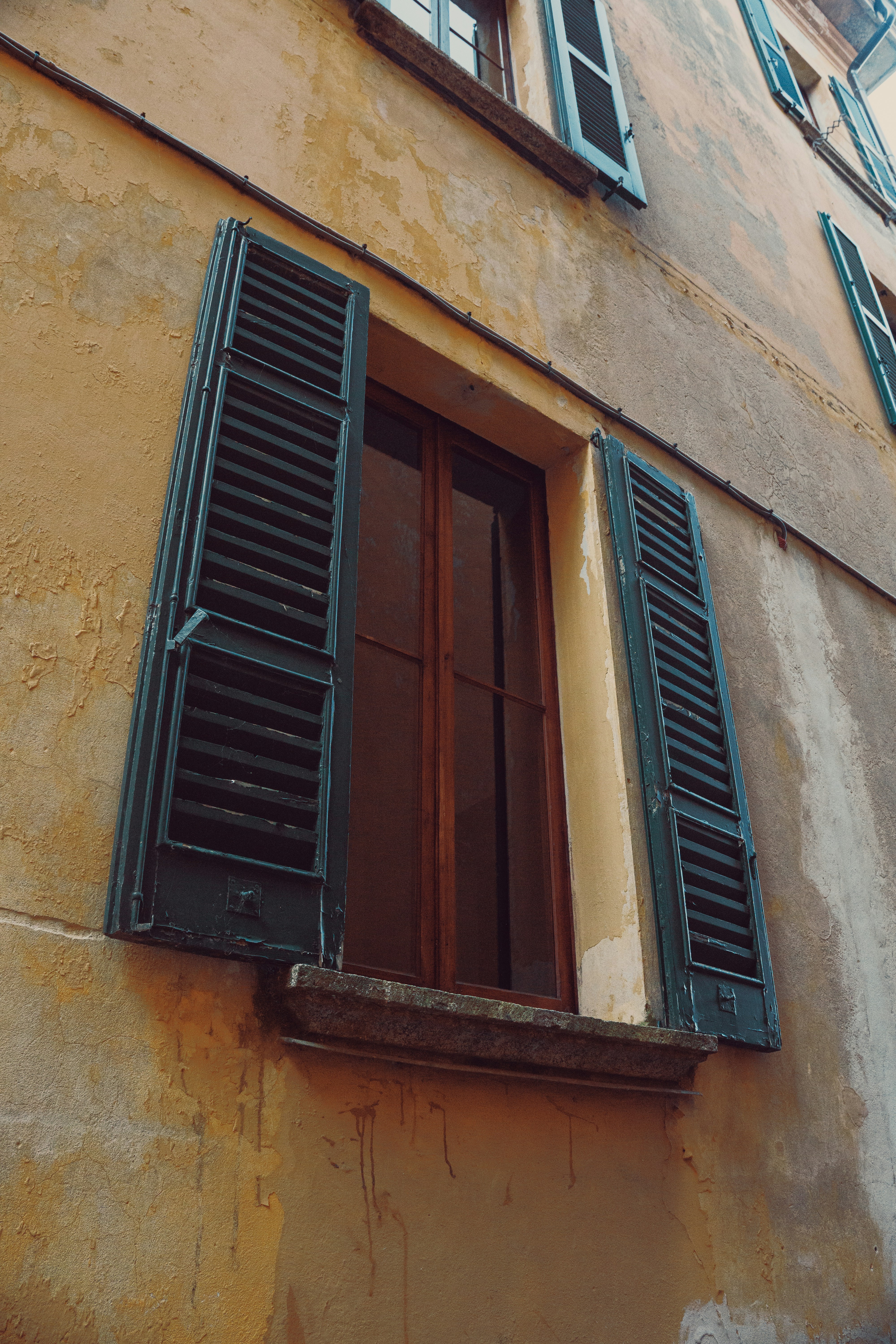 Sunlit Terrace Window: A Weathered Facade with Open Shutters