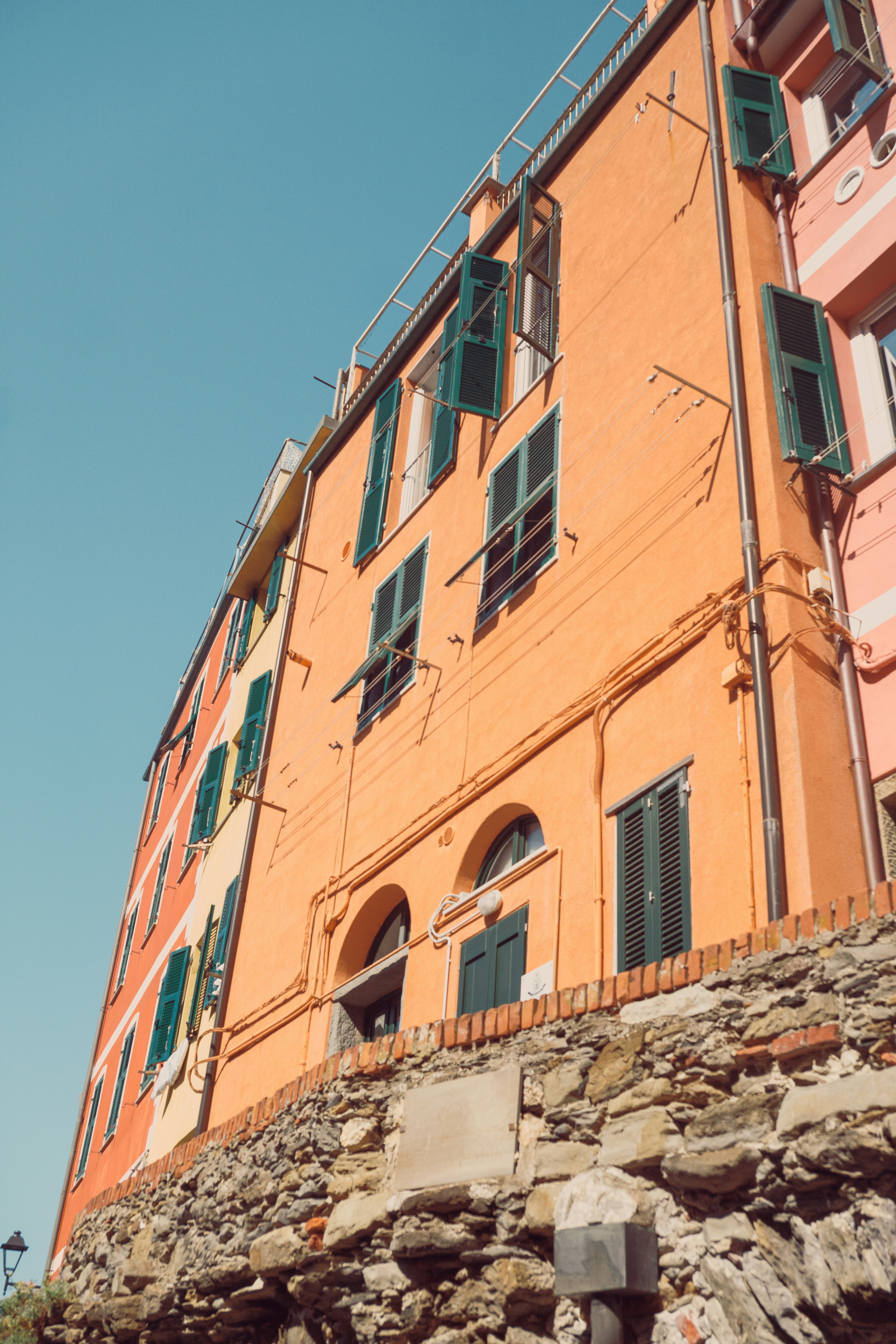 Sunlit Orange Facade with Green Shutters on a Sloped Italian Street
