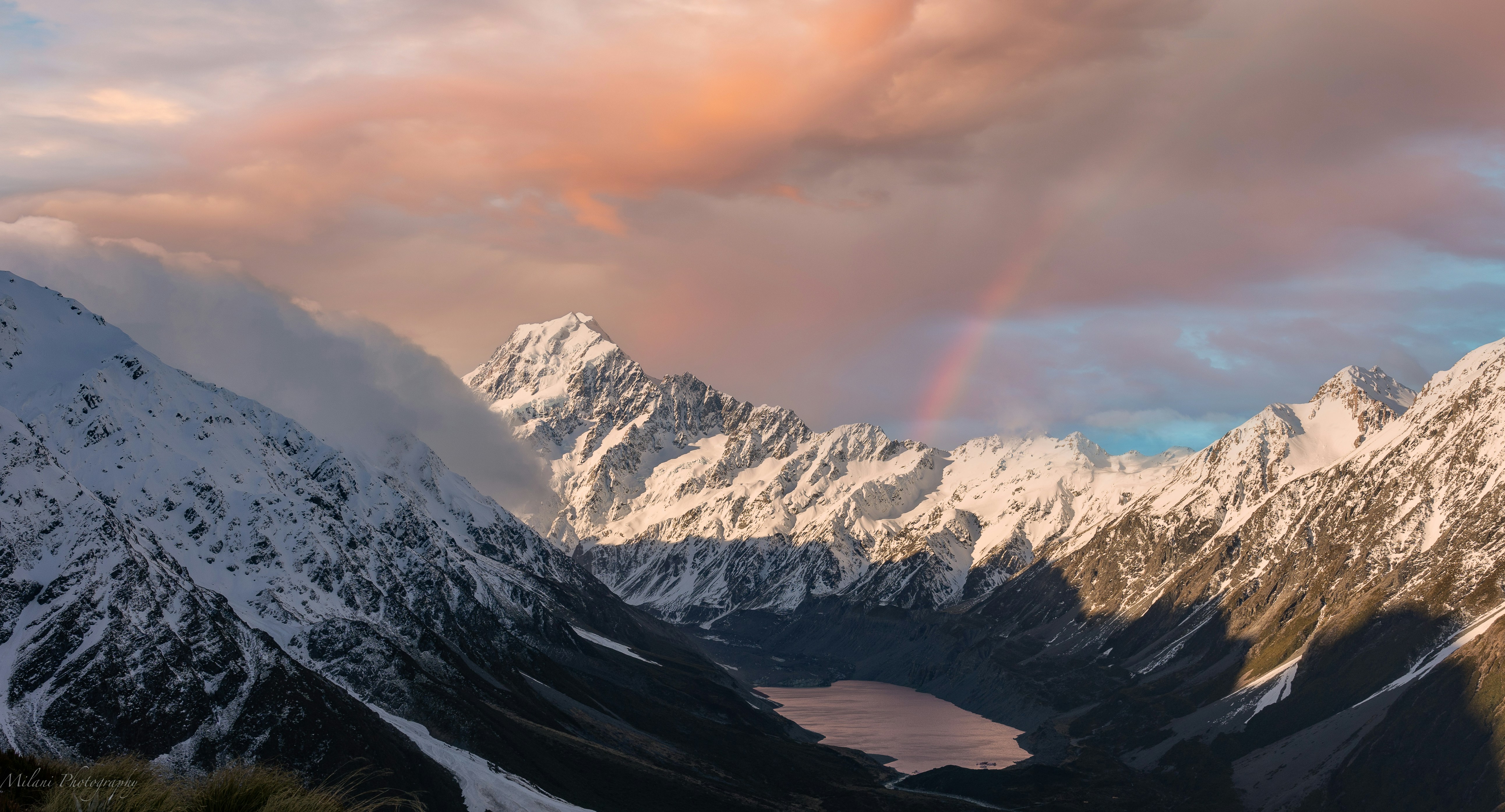 Rainbow Above Snow–Capped Peaks at Dusk