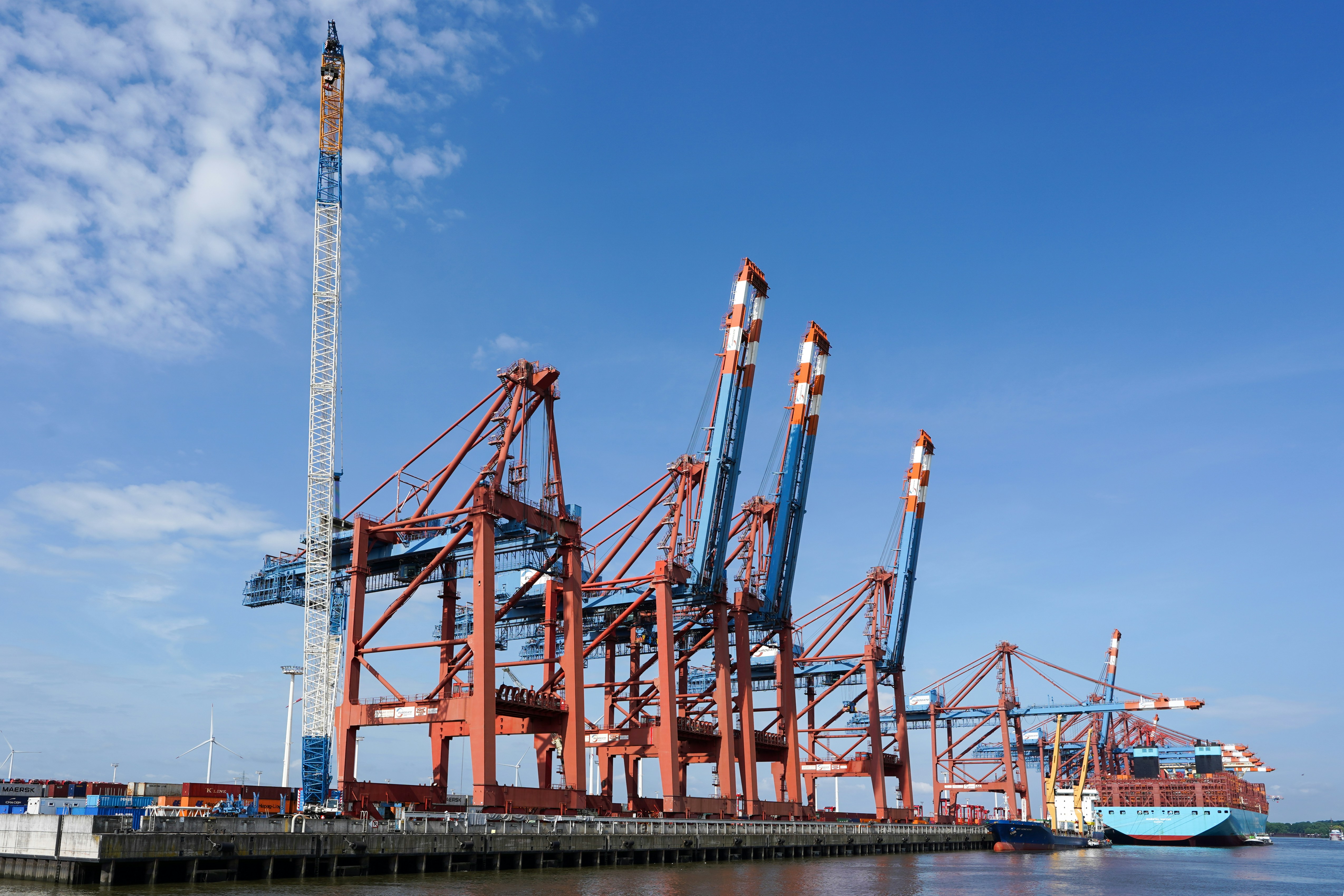 Large red container cranes at a shipping terminal under a clear blue sky.