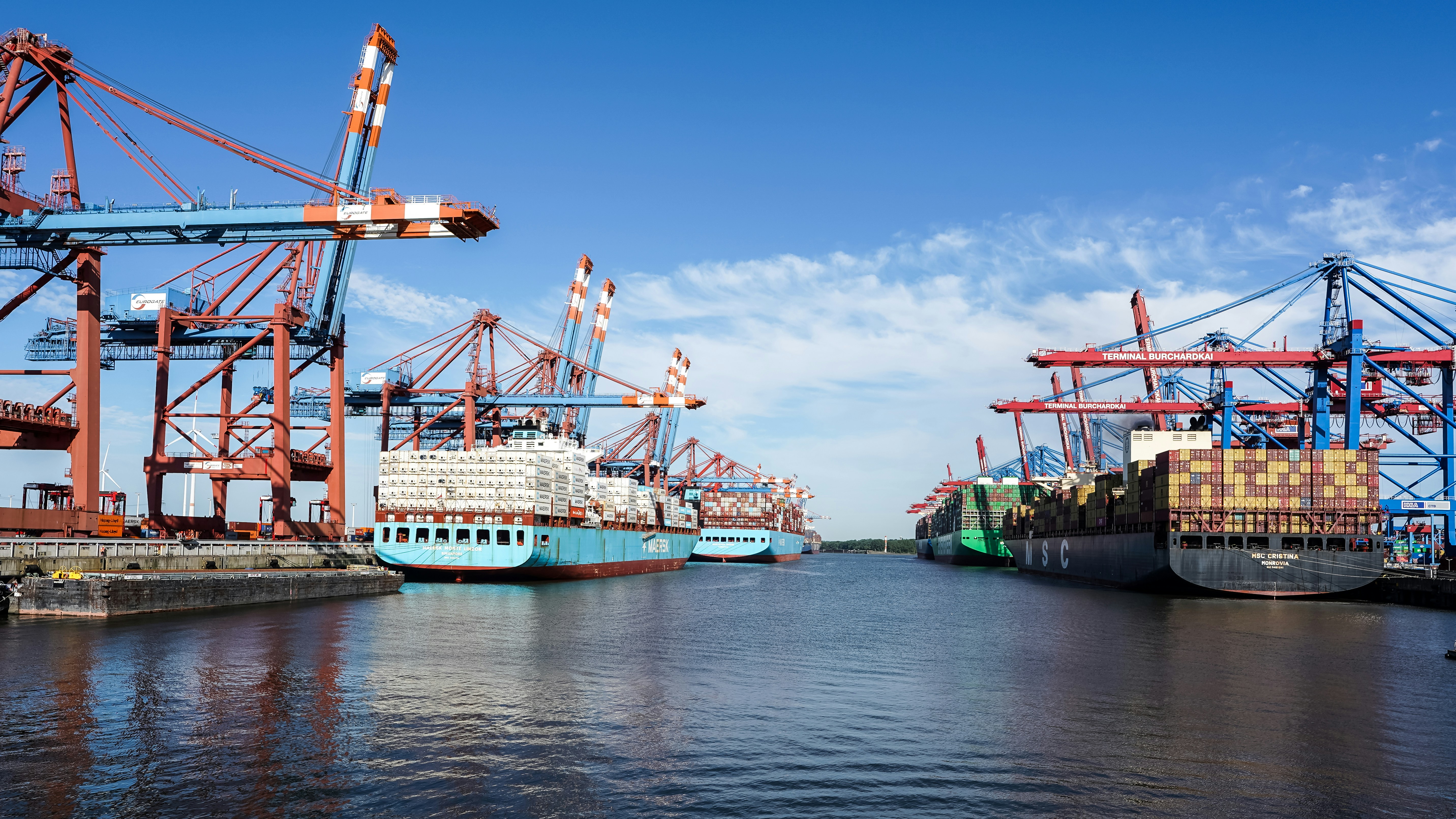Container ships docked at a busy industrial port with large red cranes.