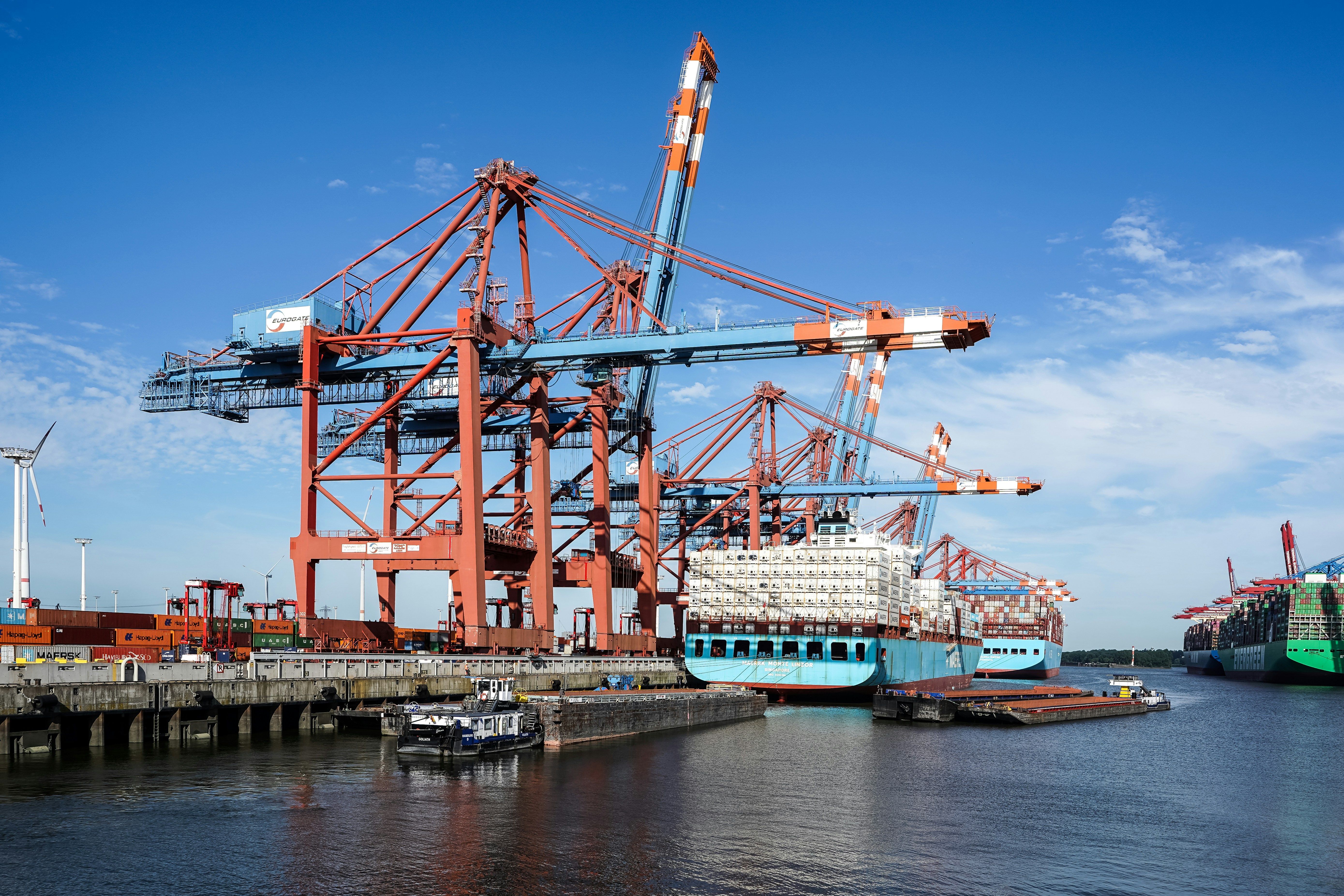 Large container ships docked at a busy industrial port with red cranes.