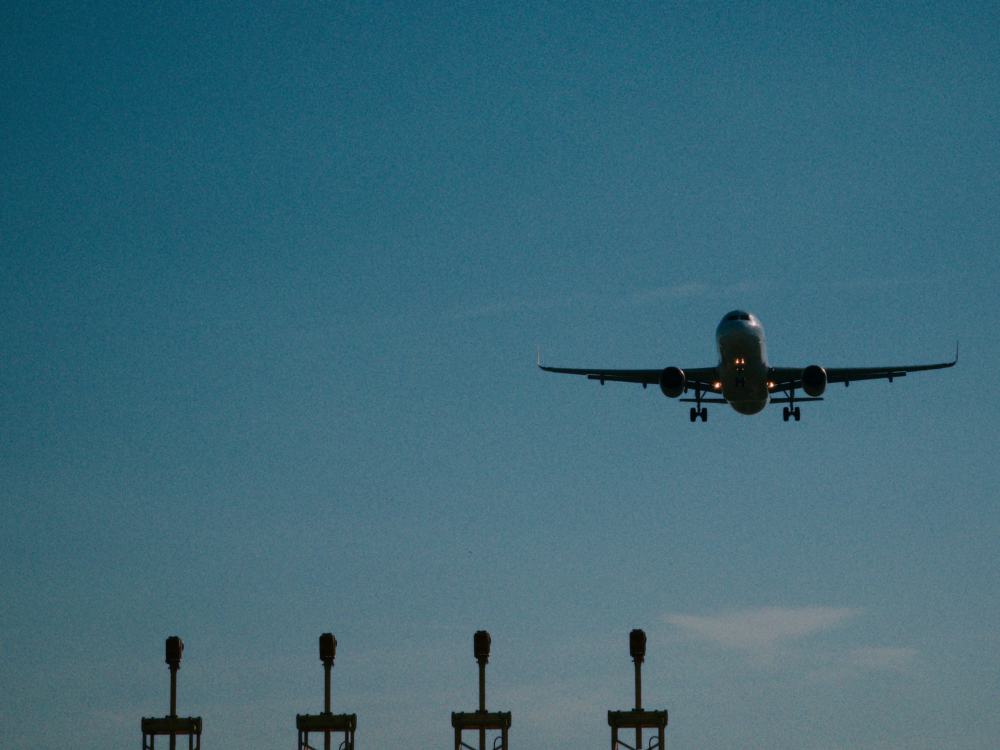 A plane drops toward the lights, still high enough to look small against the sky. The whole geometry of landing, laid out in one frame.