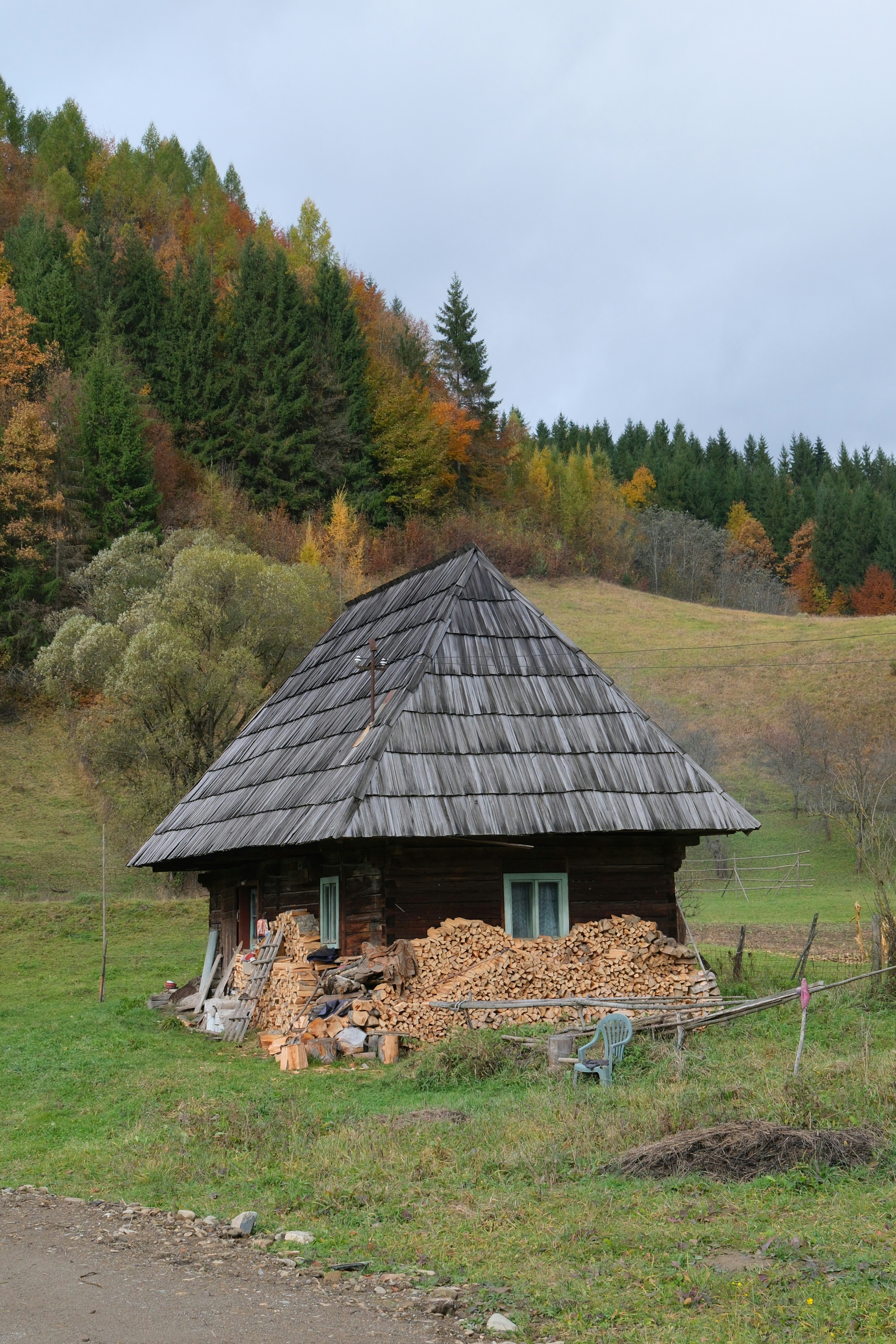 A Quiet Wooden Hut with Stacked Firewood Beneath Autumn Hills