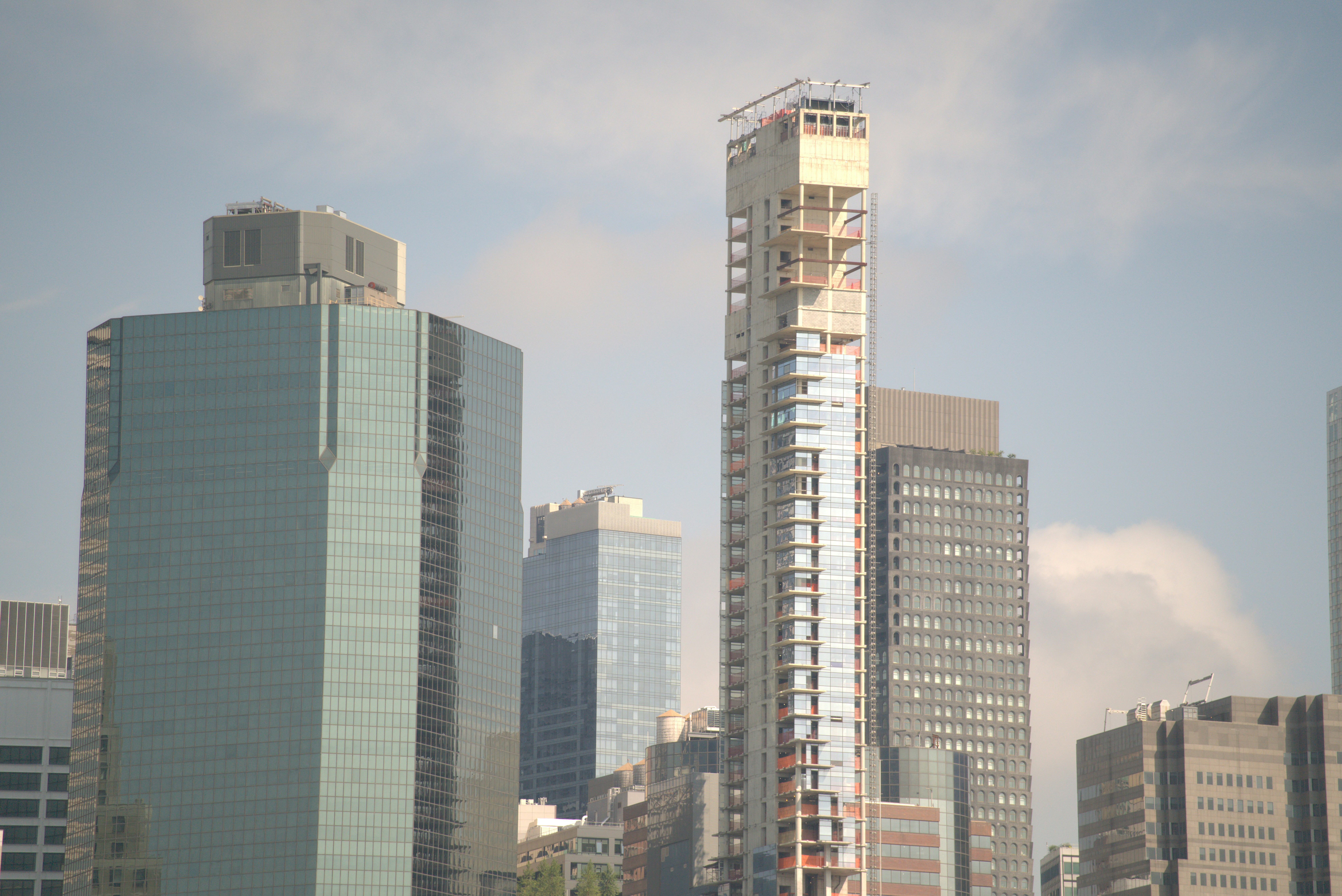 A tall skyscraper under construction among glass office buildings in a city skyline.
