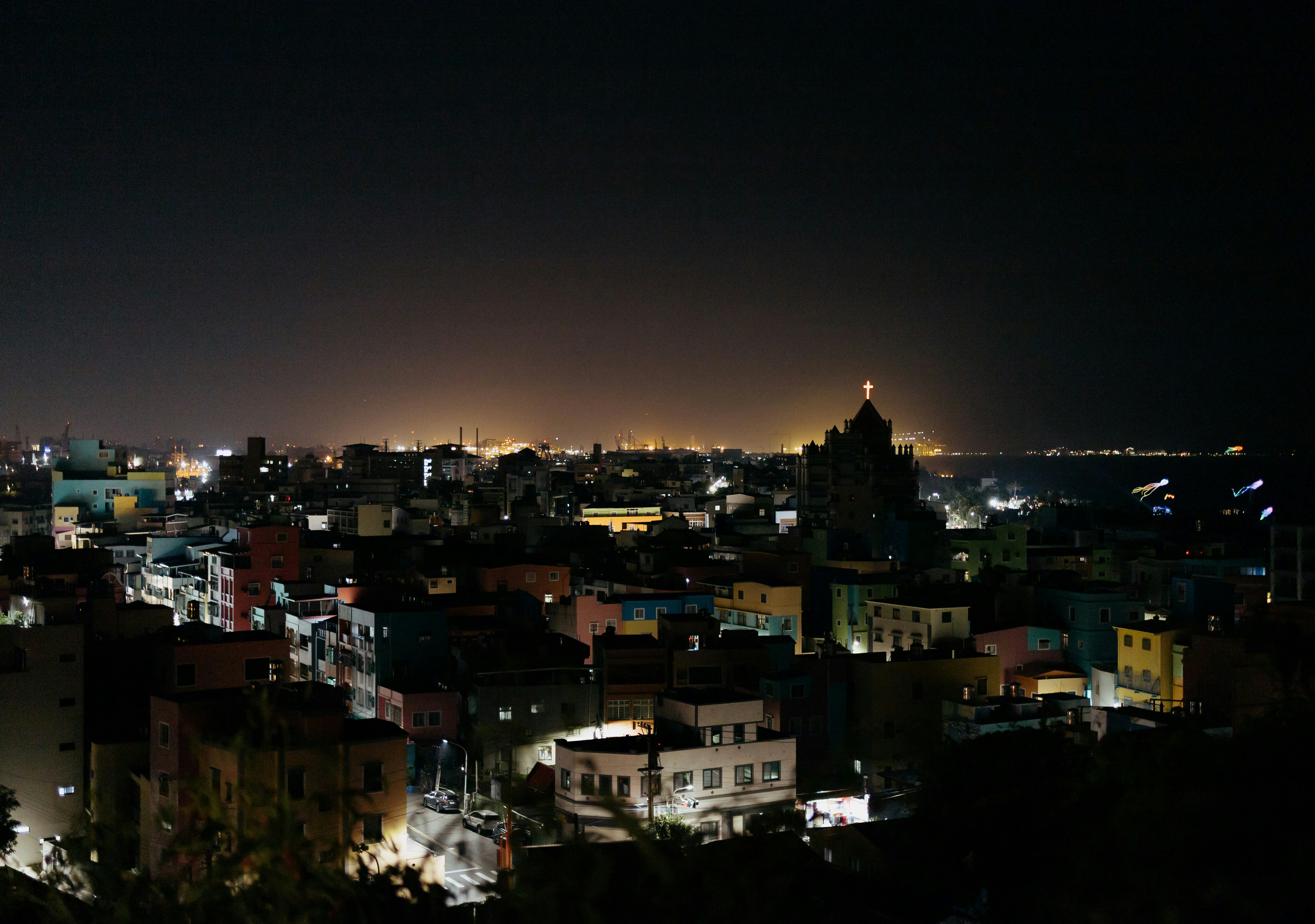 Nightscape Over a Quiet City: A Lone Church Cross Illuminates the Horizon
