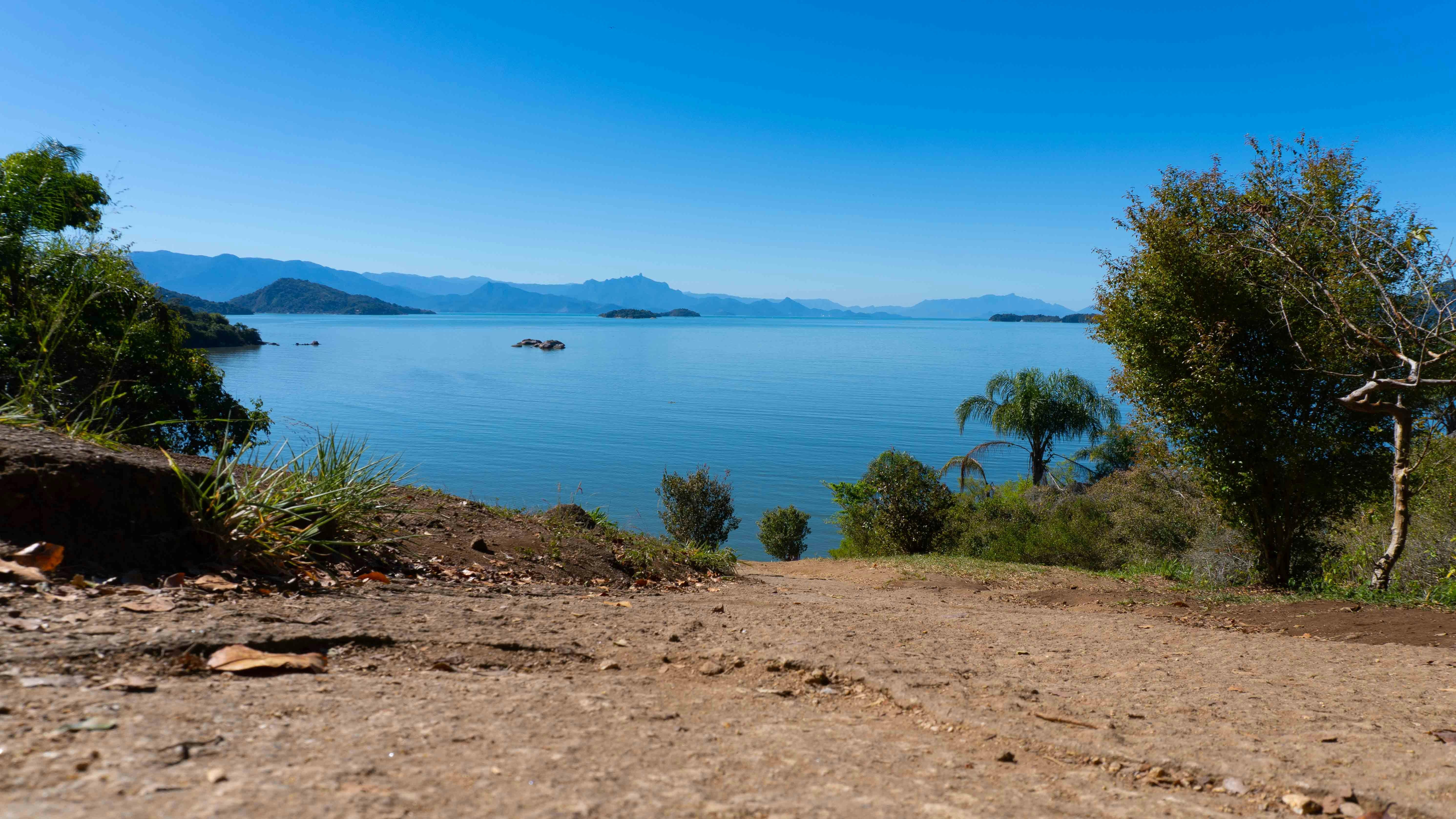 Quiet shoreline overlook: distant islands shimmer over calm blue water