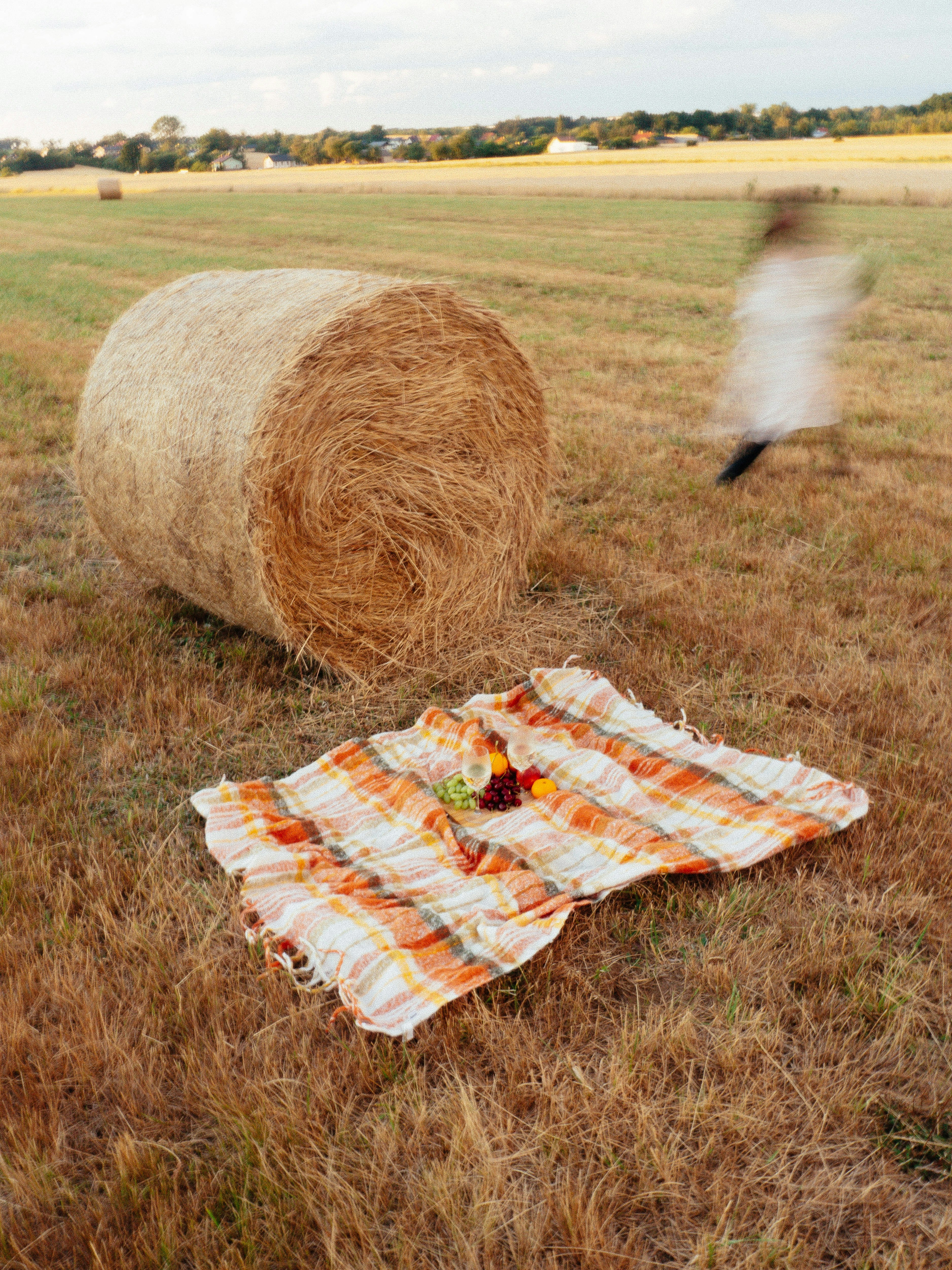 Hayfield Picnic: A lone blanket and hay bale under late afternoon light