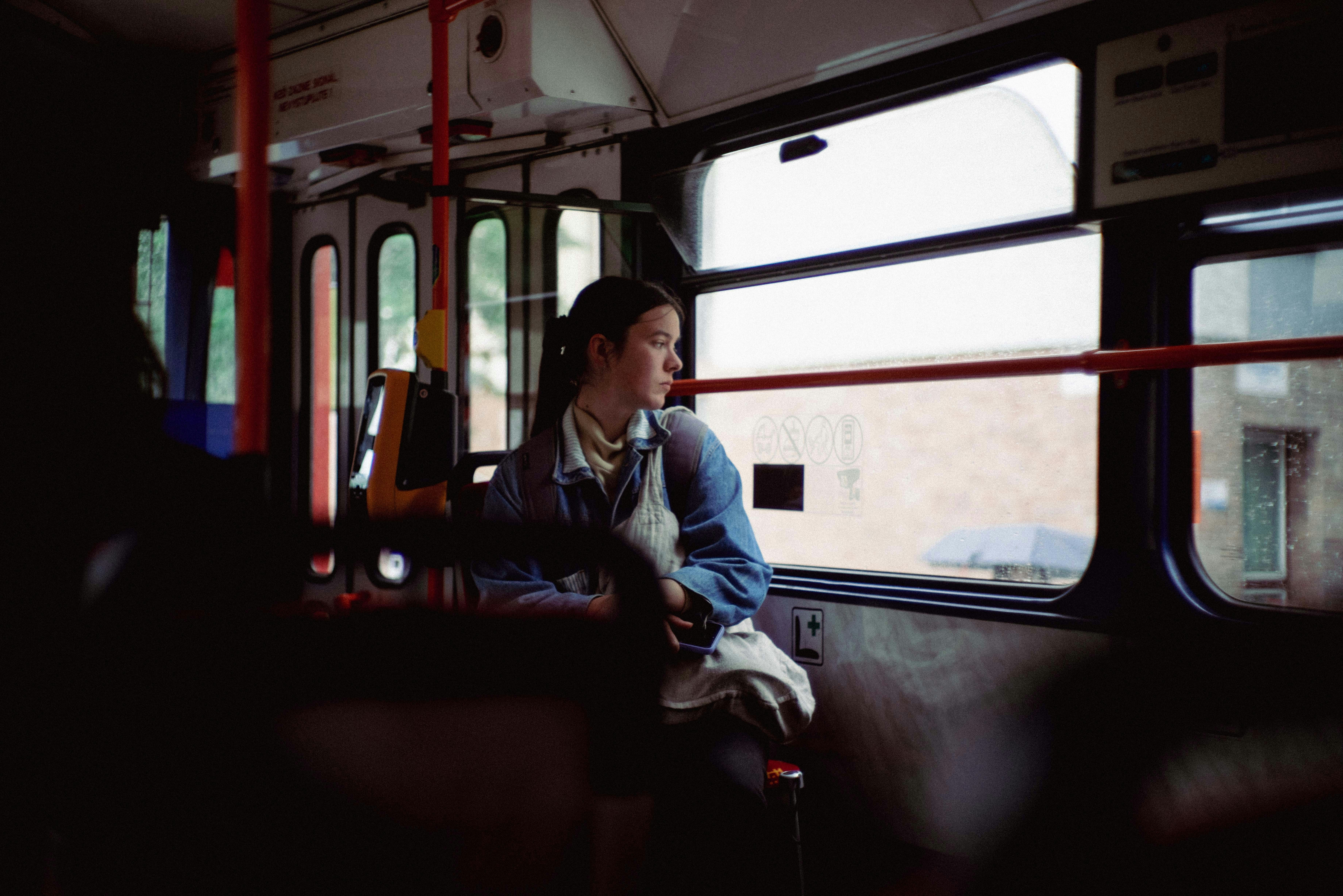 A woman in a denim jacket looking out a bus window.
