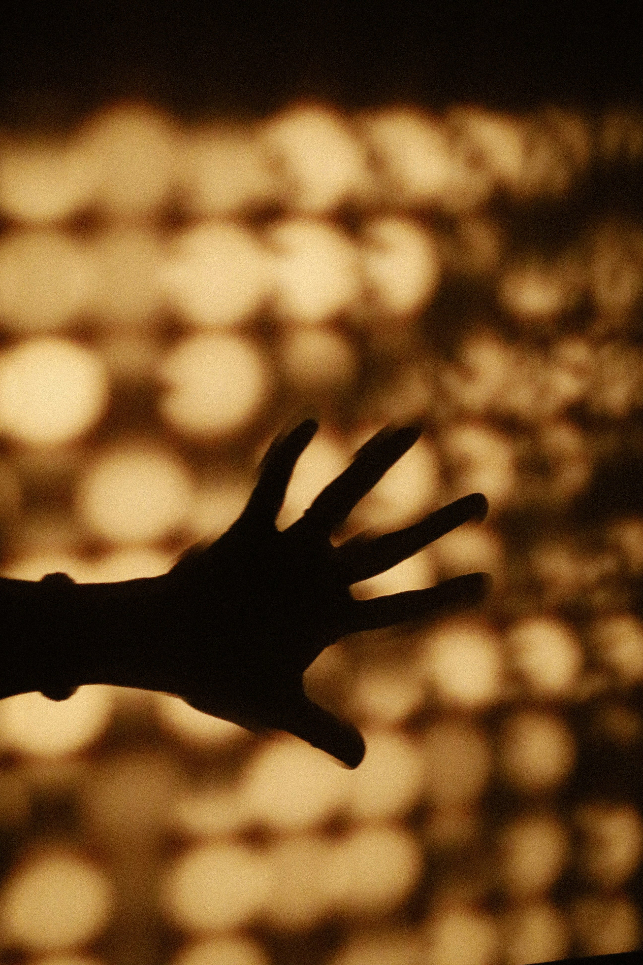 Outstretched Shadow: A Gloved Hand Reaches Toward Warm Orbs