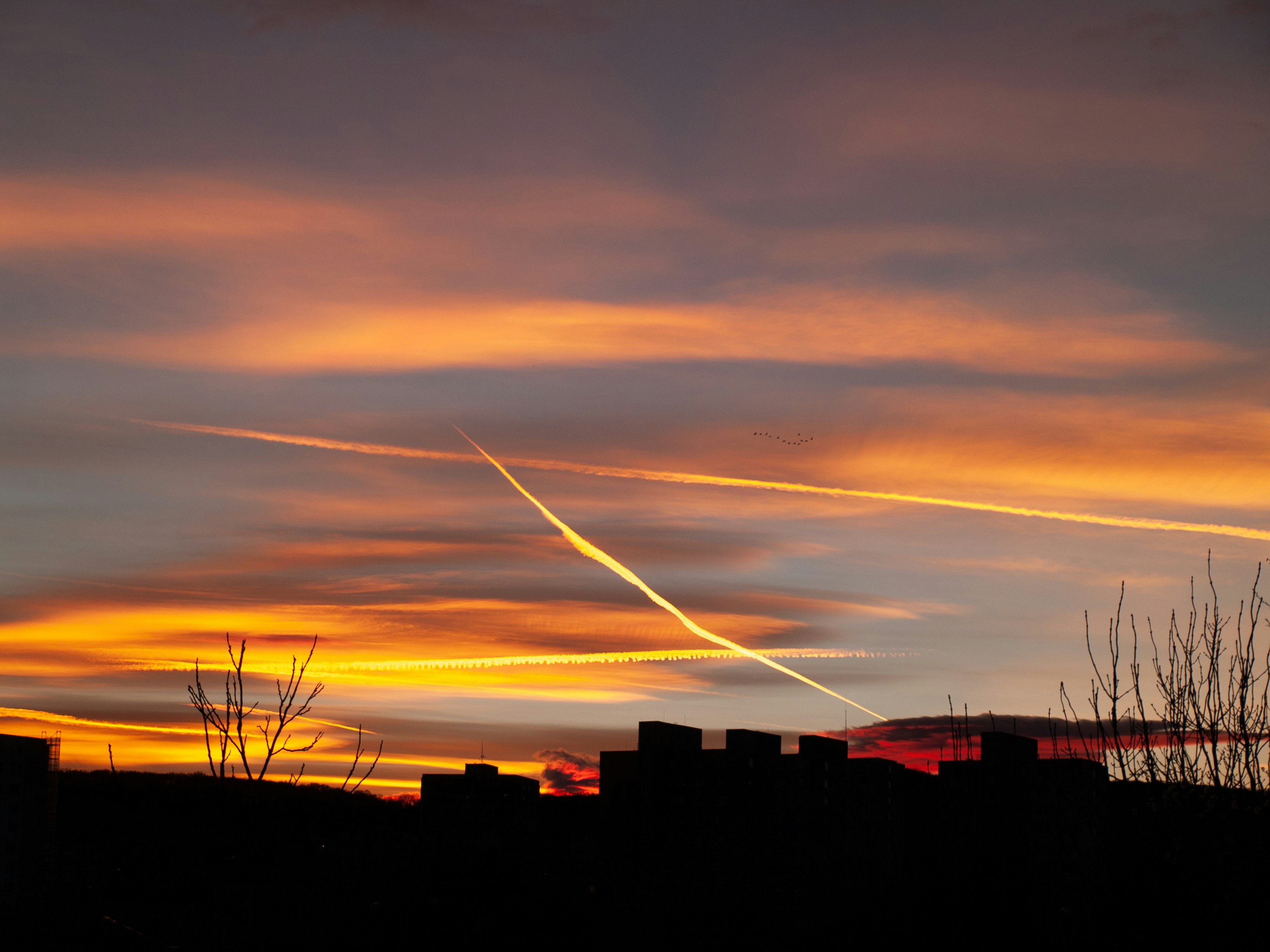 Silhouetted cityscape at sunset with a bright contrail slicing across the colorful sky.