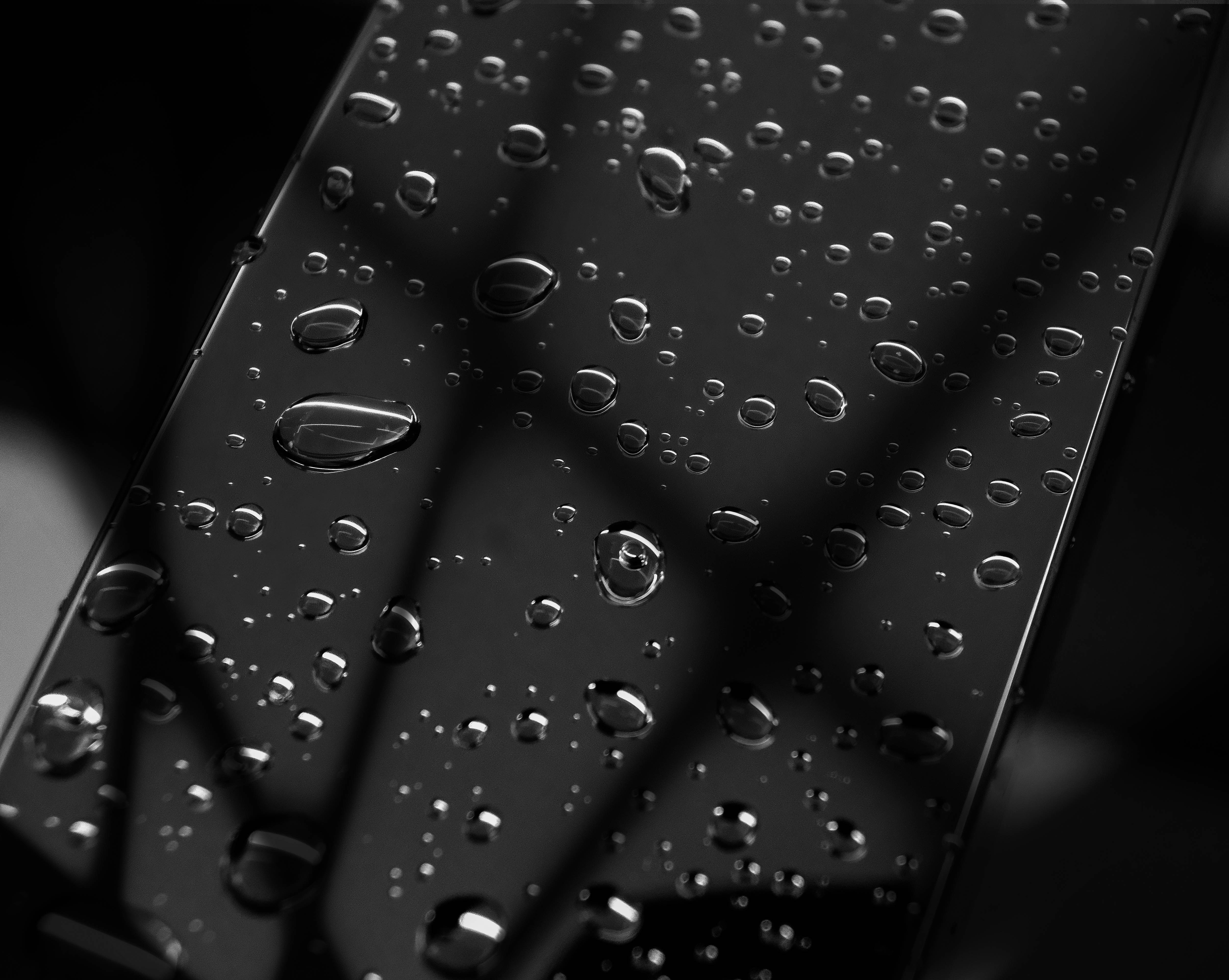 Close-up of glossy metallic surfaces with scattered water droplets, highlighting texture and reflections on a sleek, monochrome panel.