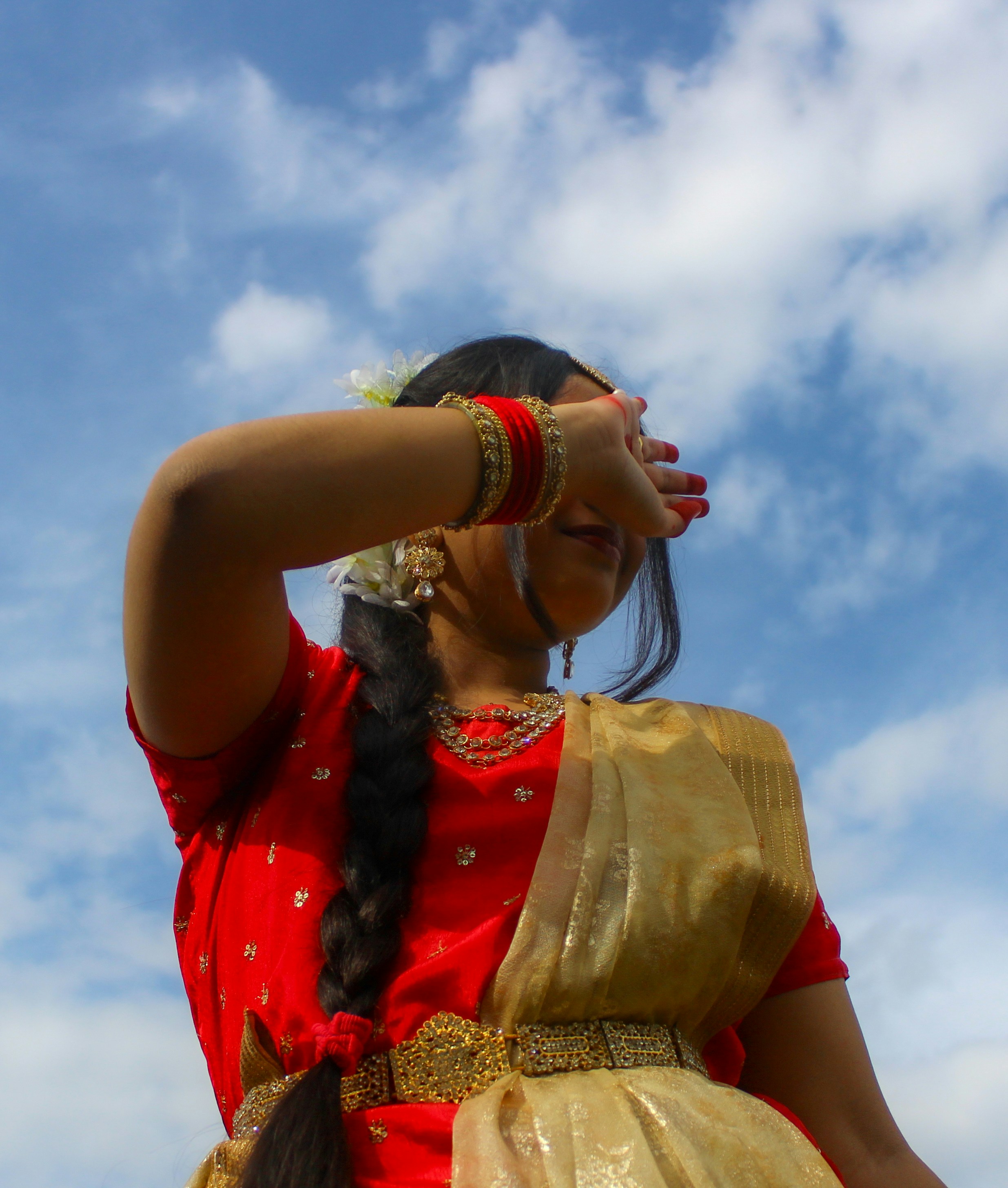 Sunlit Celebration: A Traditional Red and Gold Attire Against a Sky-Blue Backdrop