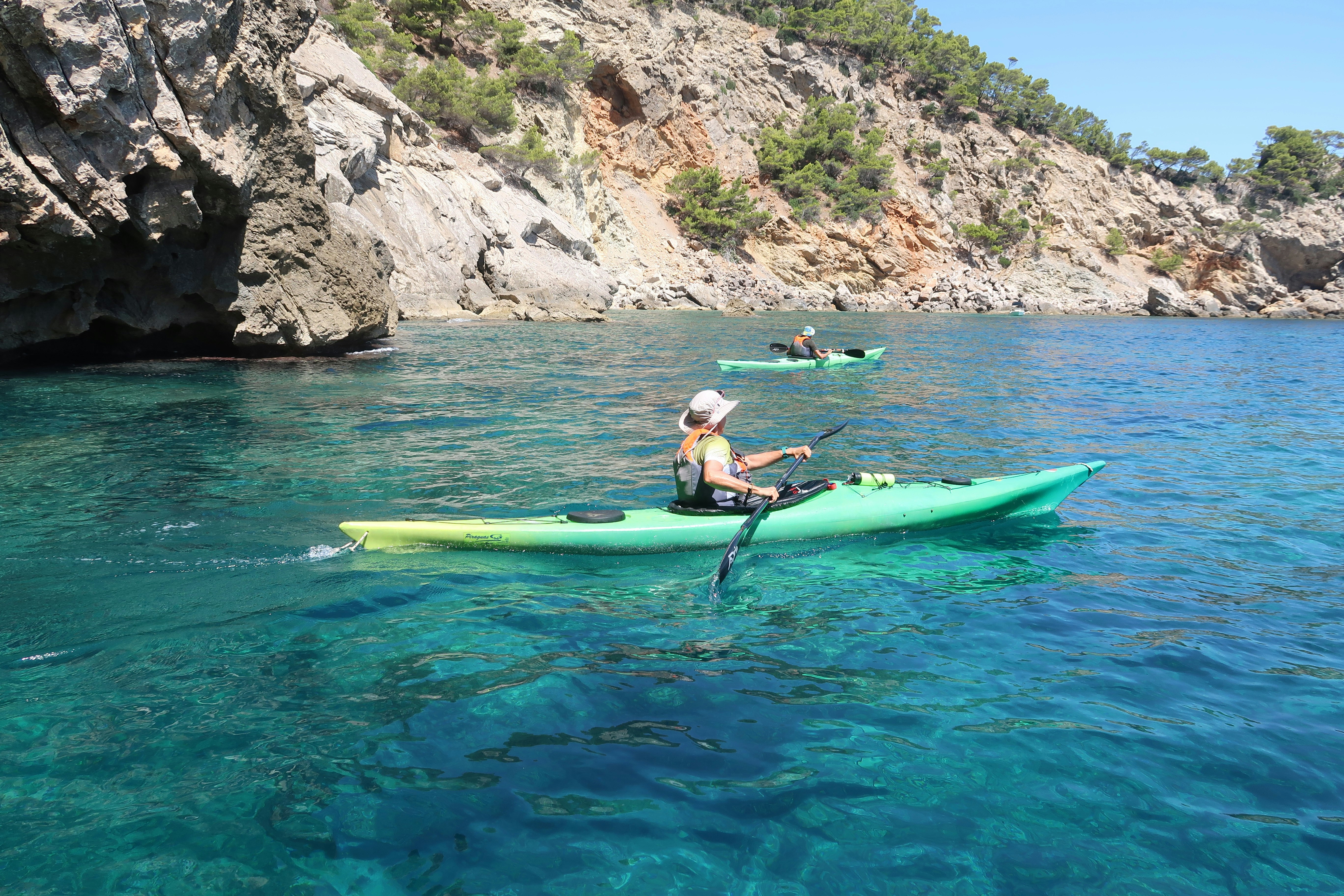 Two Kayakers Explore Turquoise Waters Near Rugged Canyon Walls