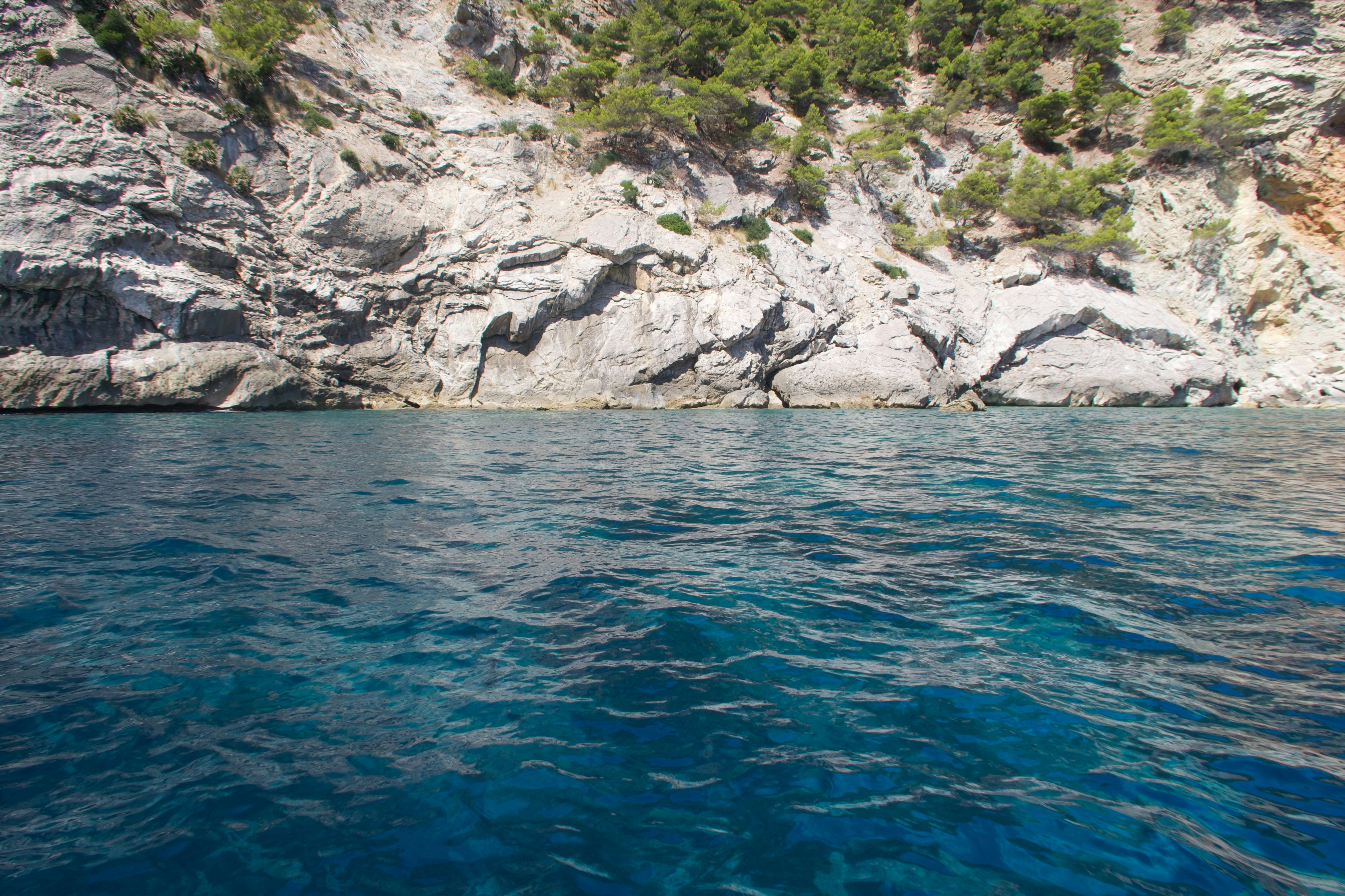 Rocky shoreline over a calm blue sea, where rugged cliffs meet clear water
