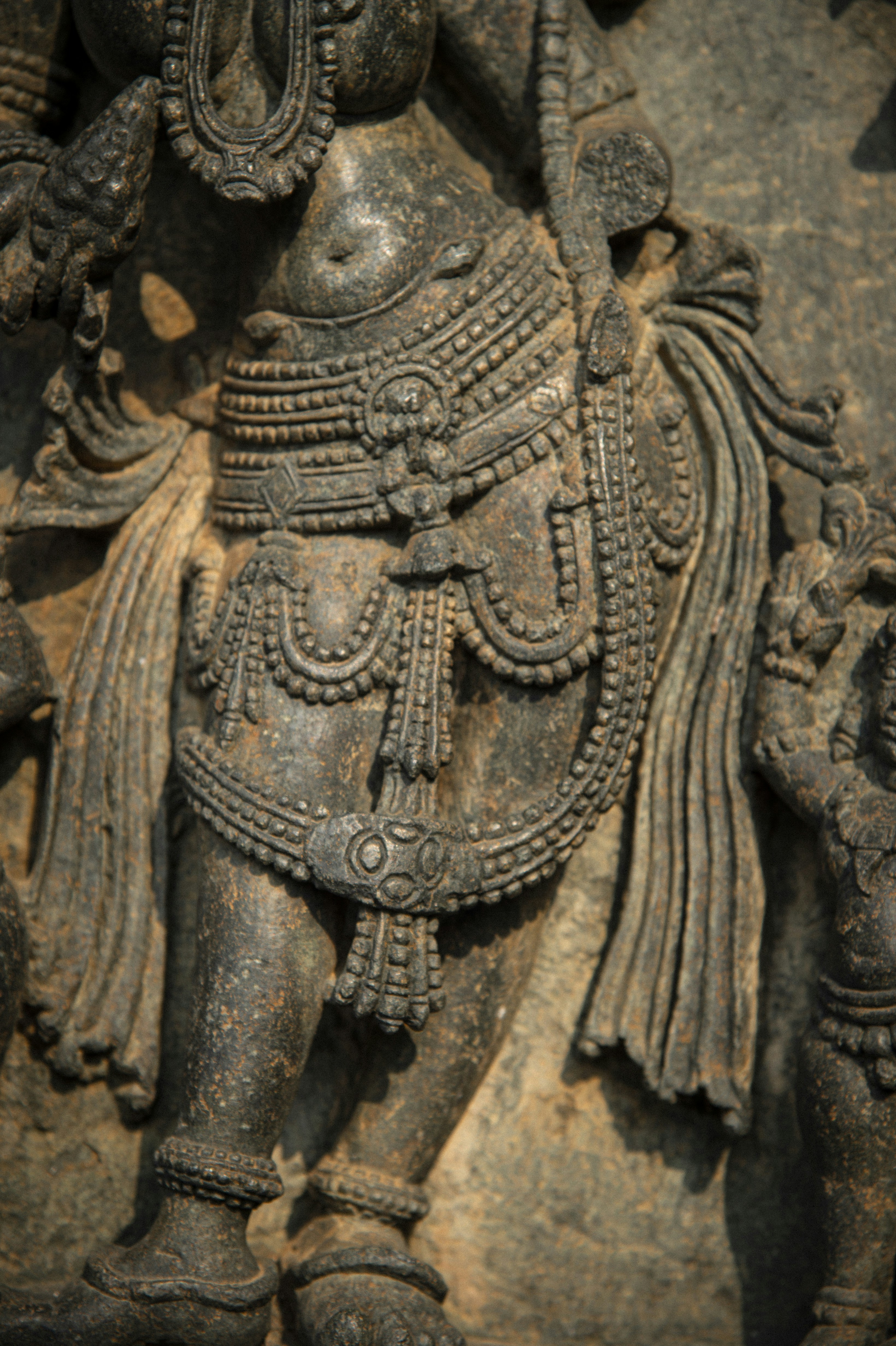 Ornate Stone Adornment: A Weathered Deity Adorned with Multilayered Jewelry