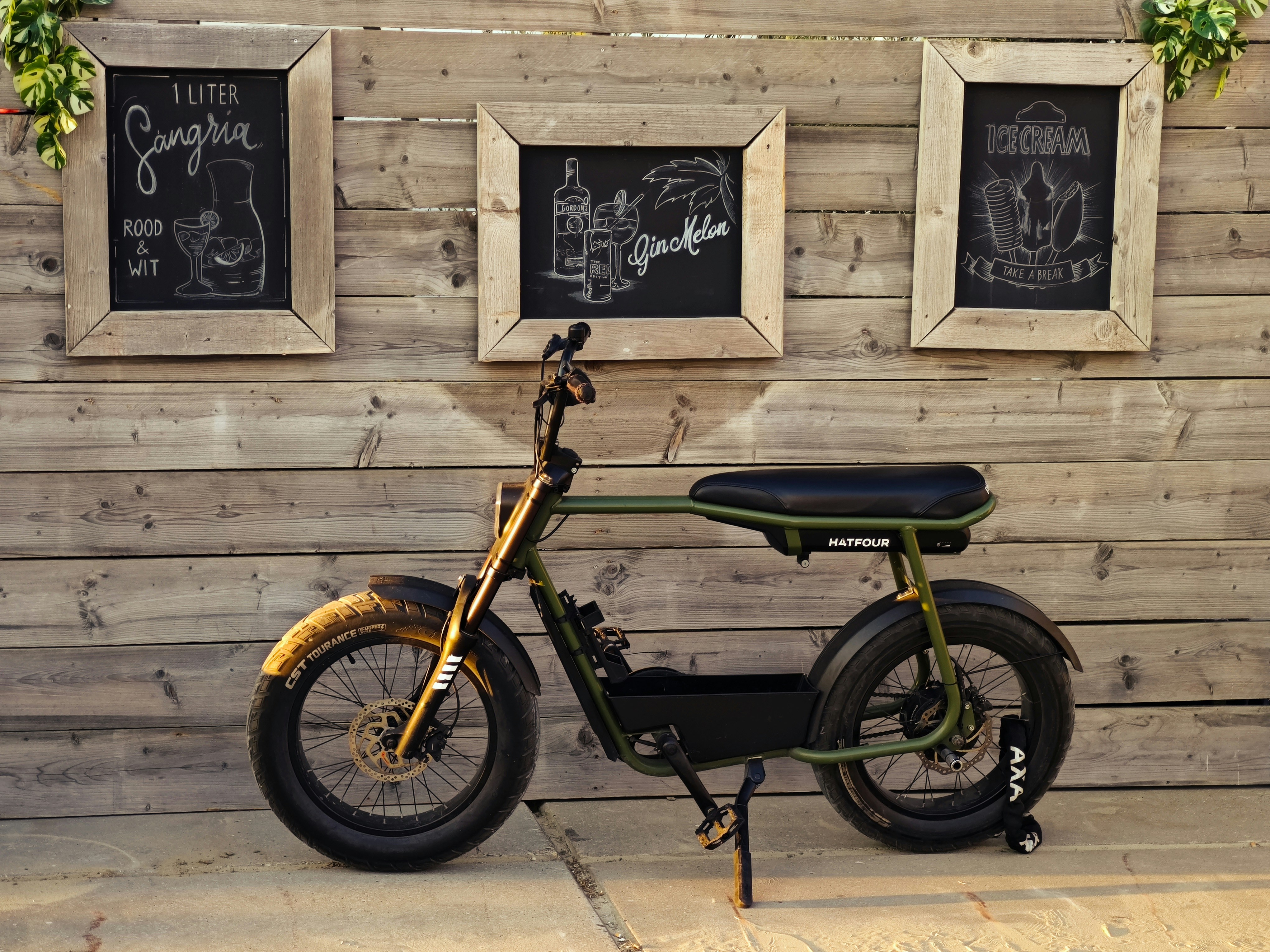 Electric bike parked against a rustic wooden wall with framed chalkboard art; a simple, utilitarian scene highlighting daily street design.
