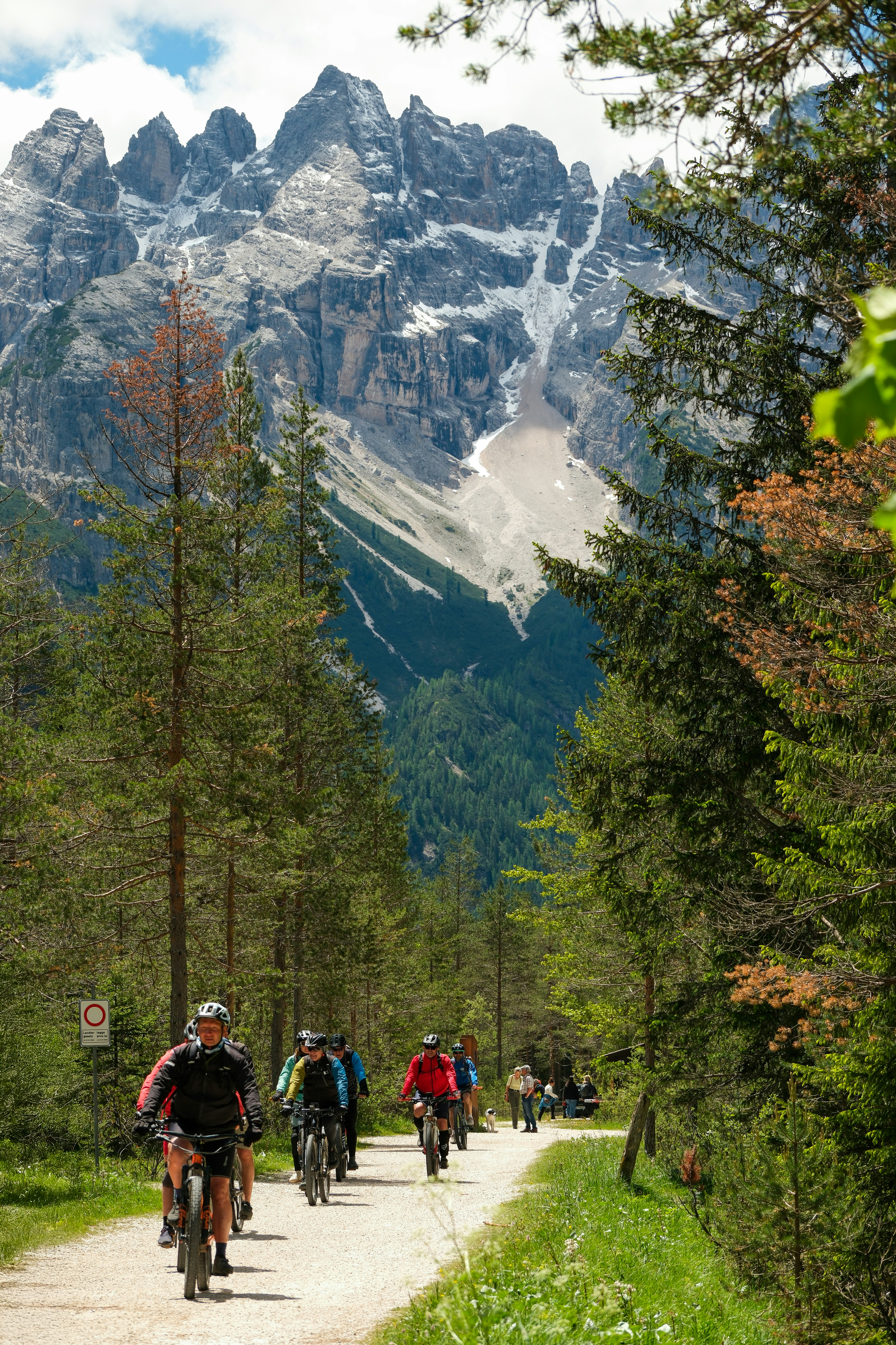 Cyclists descend a sunlit alpine trail beneath jagged peaks