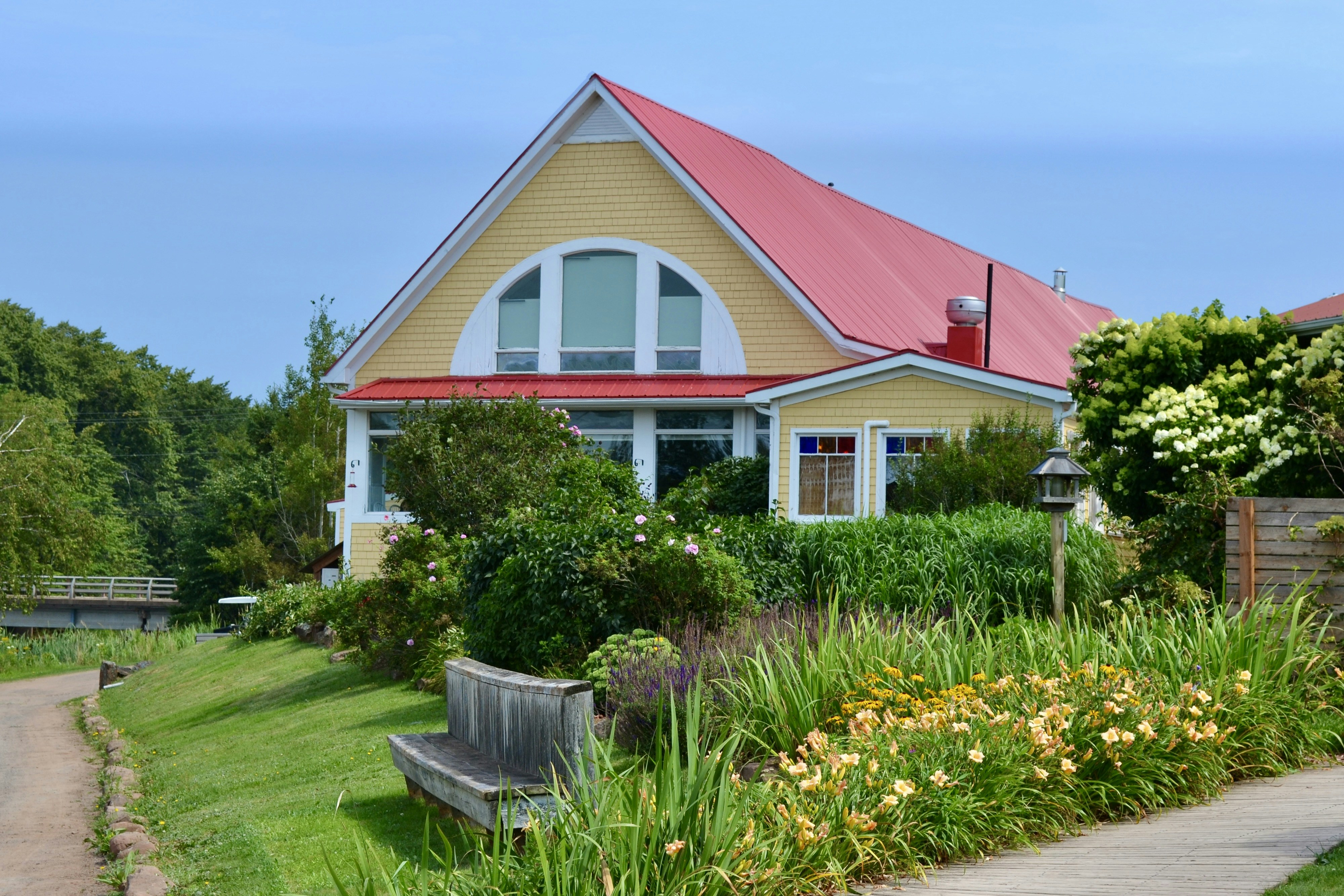 Sunlit Cottage Oasis: A Cheerful Yellow House Beside a Blossoming Garden