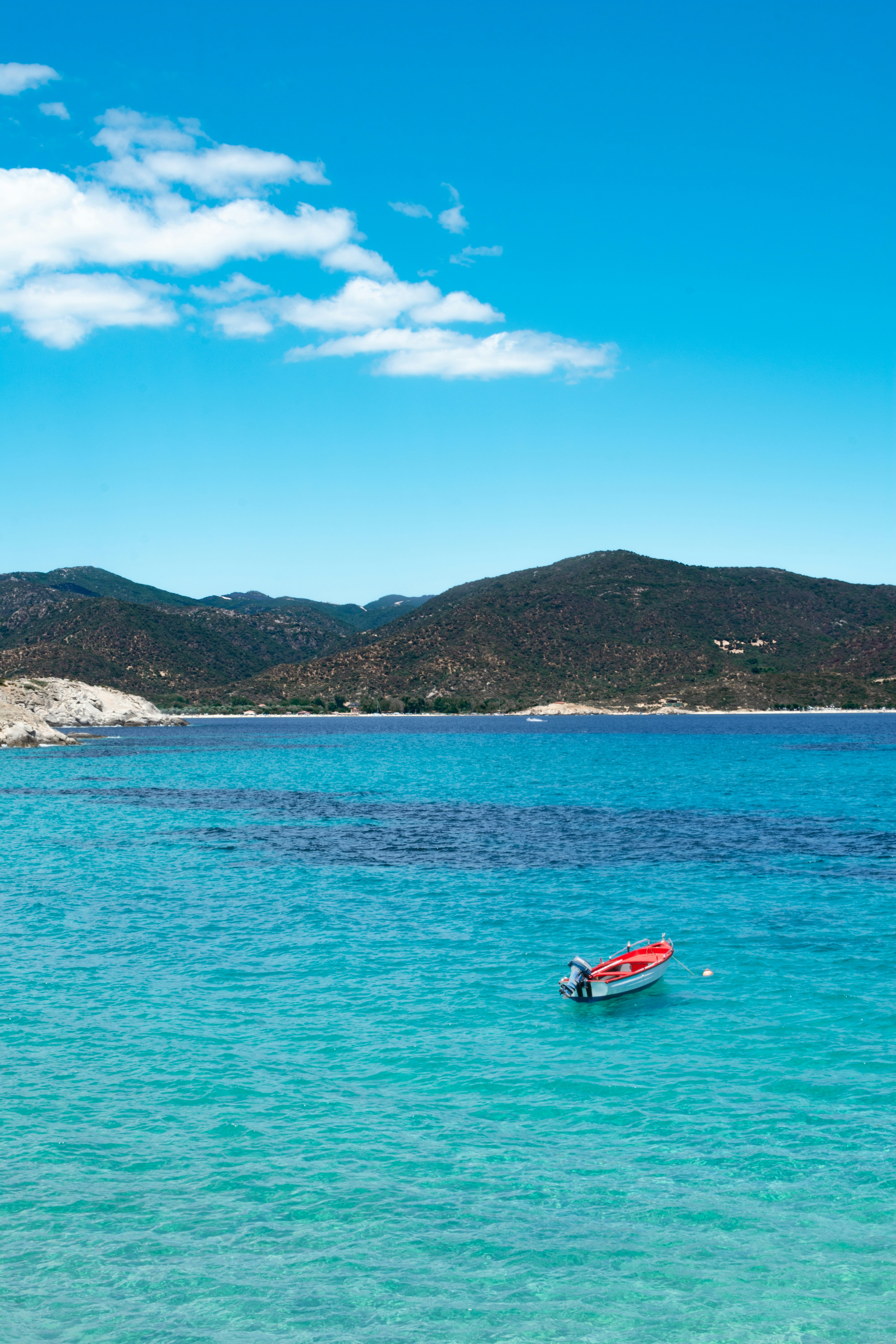 Azure Bell: Lone Boat Drifts in Turquoise Seas Beneath a Summer Sky