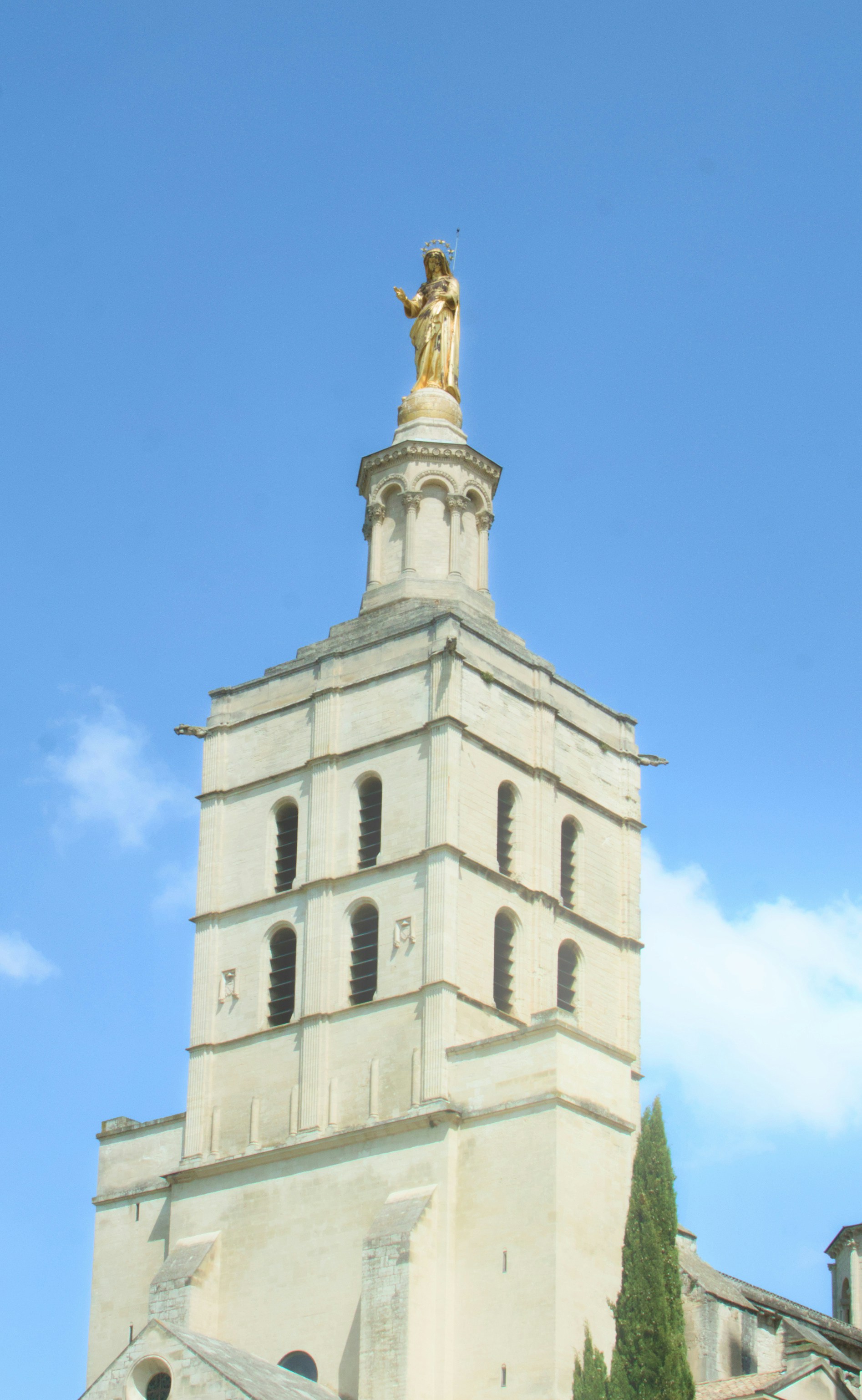 Golden statue crowns a stone spire against a clear blue sky