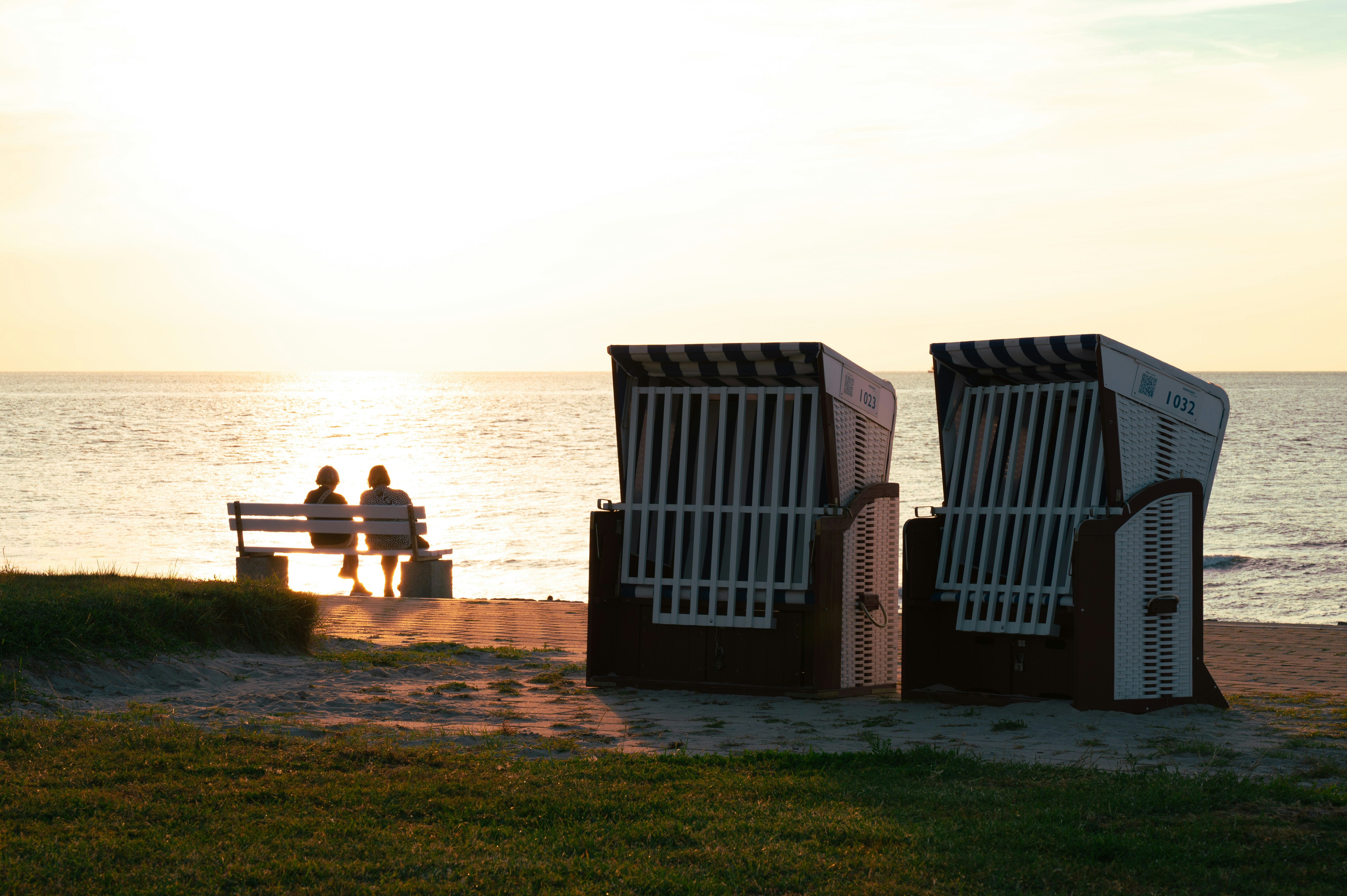 Sunlit shoreline with two silhouette figures and striped beach chairs
