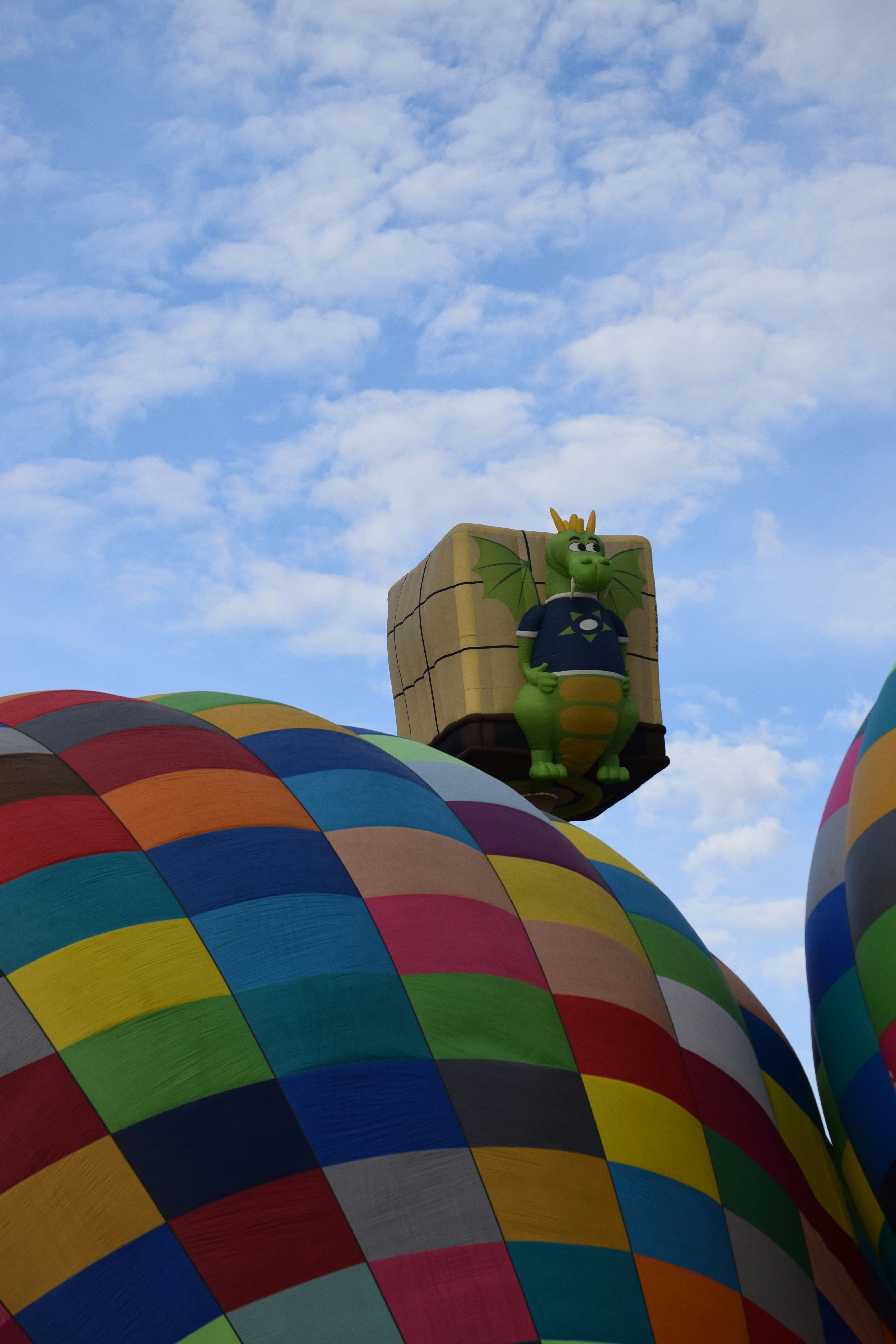 Colorful hot-air balloons fill the frame as a small dragon figure sits atop a basket against a bright blue sky.