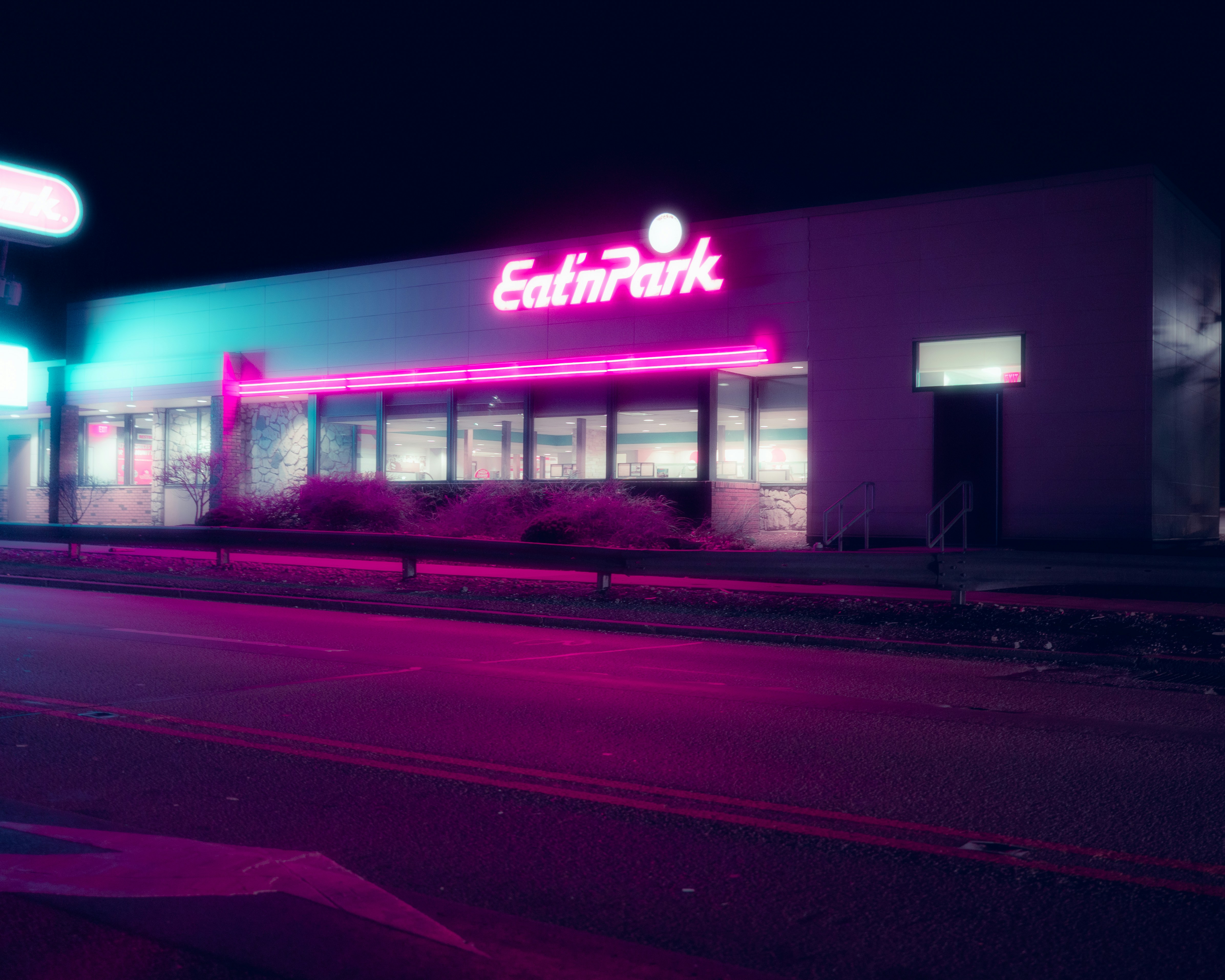 Neon-lit Eat’nPark storefront bathed in pink and blue hues, quiet street in foreground; a moody, low-light exterior shot highlighting signage and reflective surfaces. Logo/venue exterior.