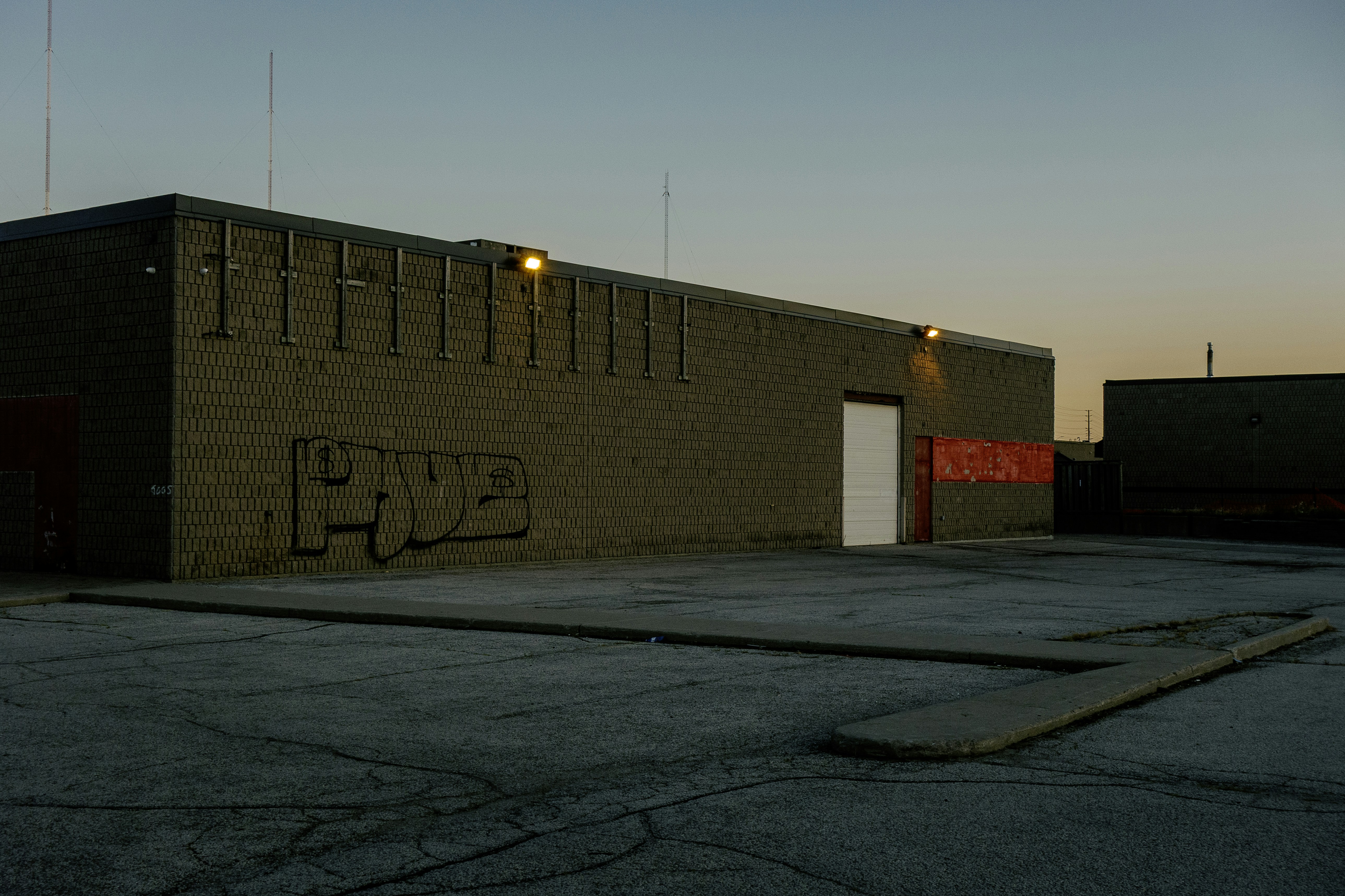 Industrial warehouse bathed in the warm glow of dusk, with a graffiti-ed wall and a single illuminated doorway.