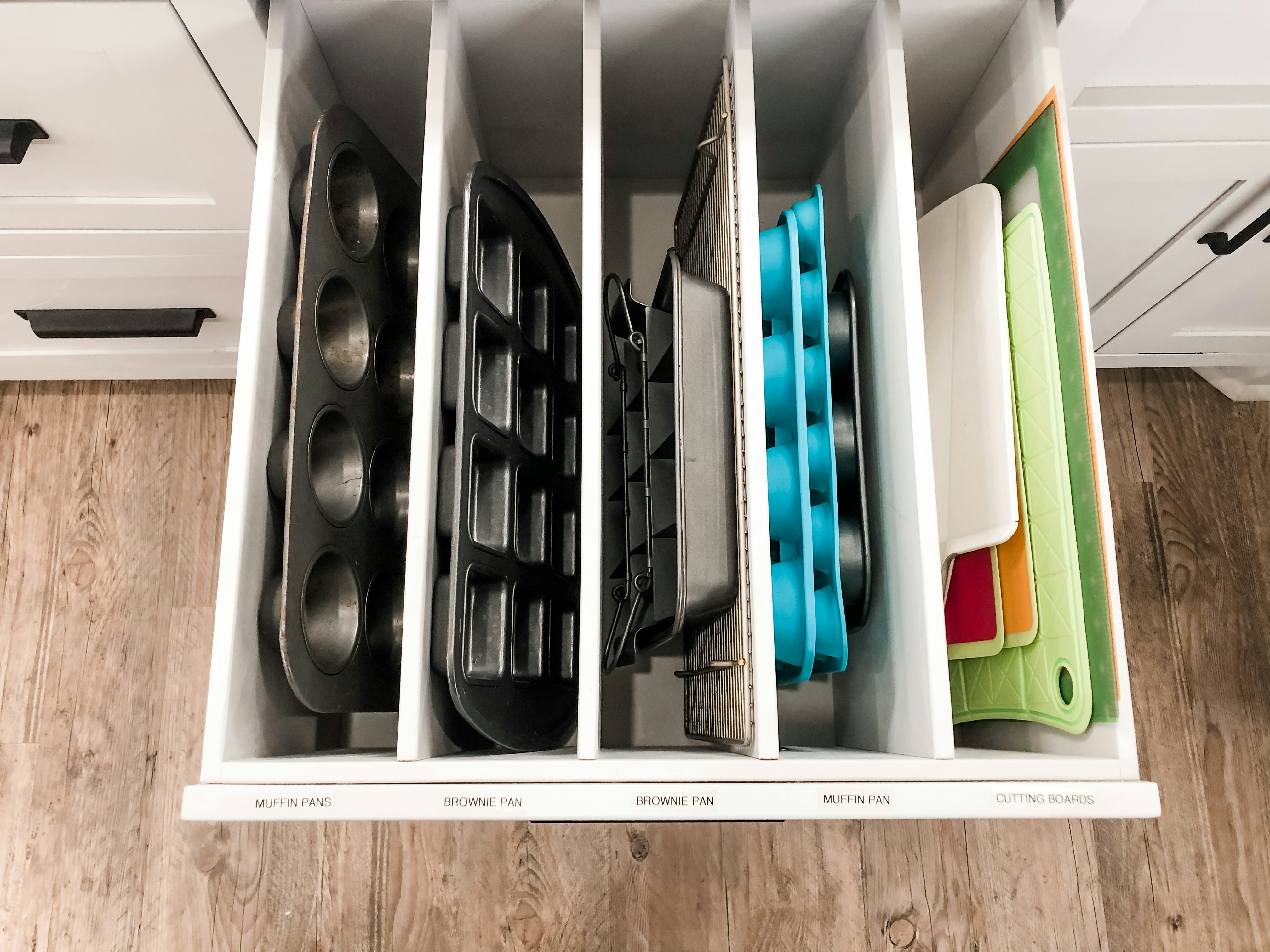 Stacked utensil dividers hold muffin tins, baking trays, and utensil inserts in a pull-out drawer with labeled compartments.