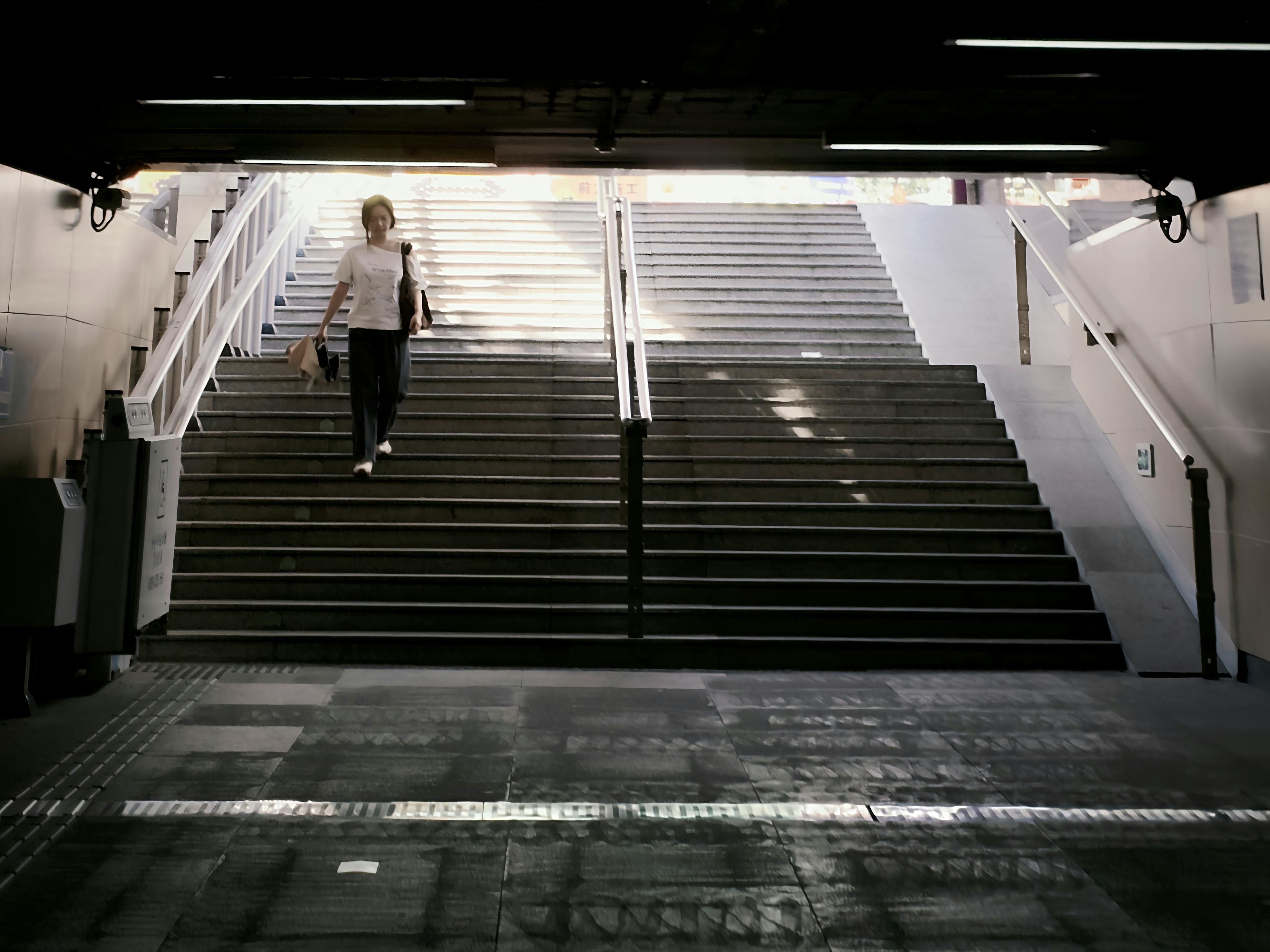 A woman walking down concrete stairs in a sunlit underpass.