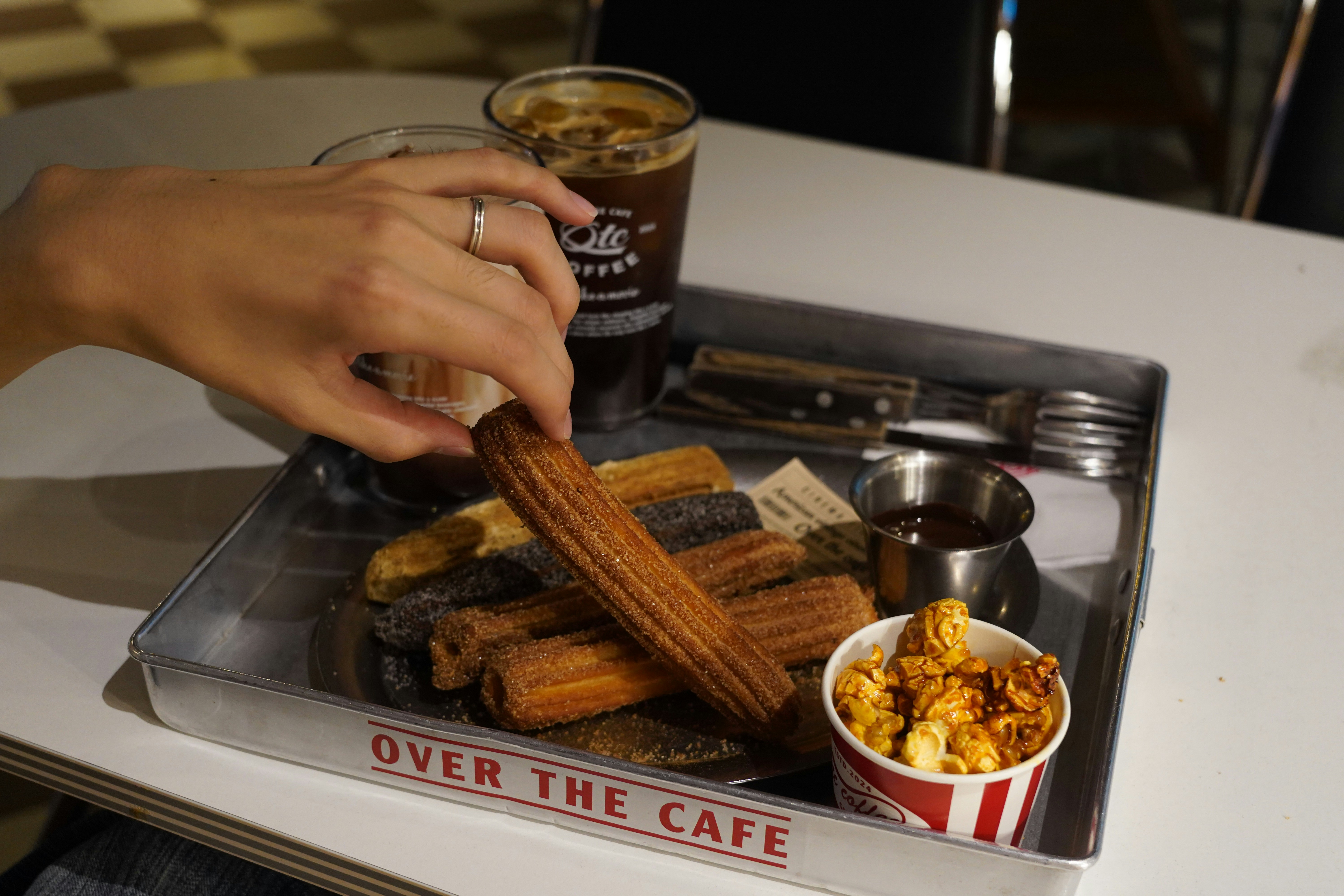 Hand Grasping a Churro at a Café Tray