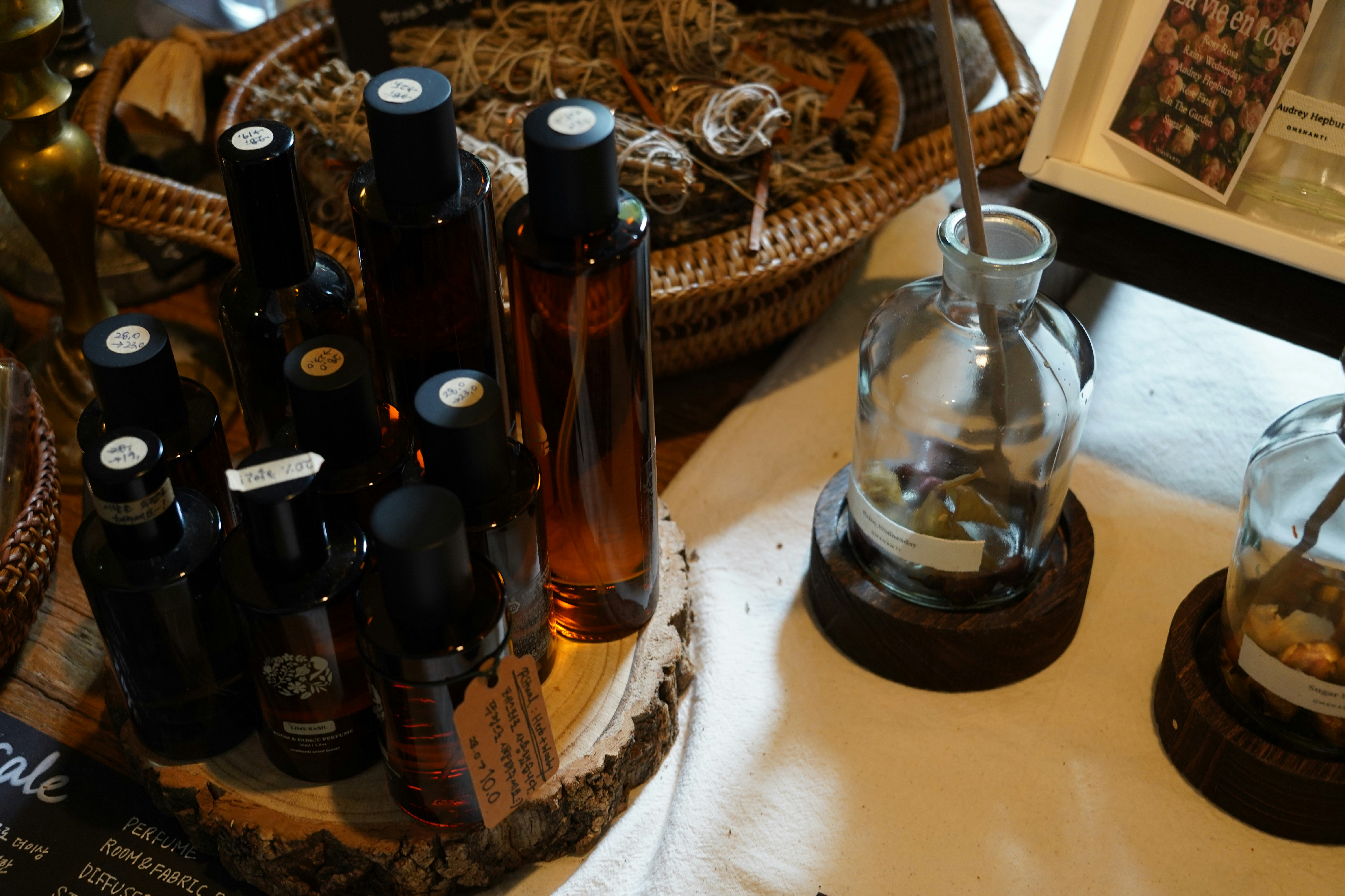 Small fragrance bottles arranged on a wooden slice display with other glass vessels in a softly lit shop setting.