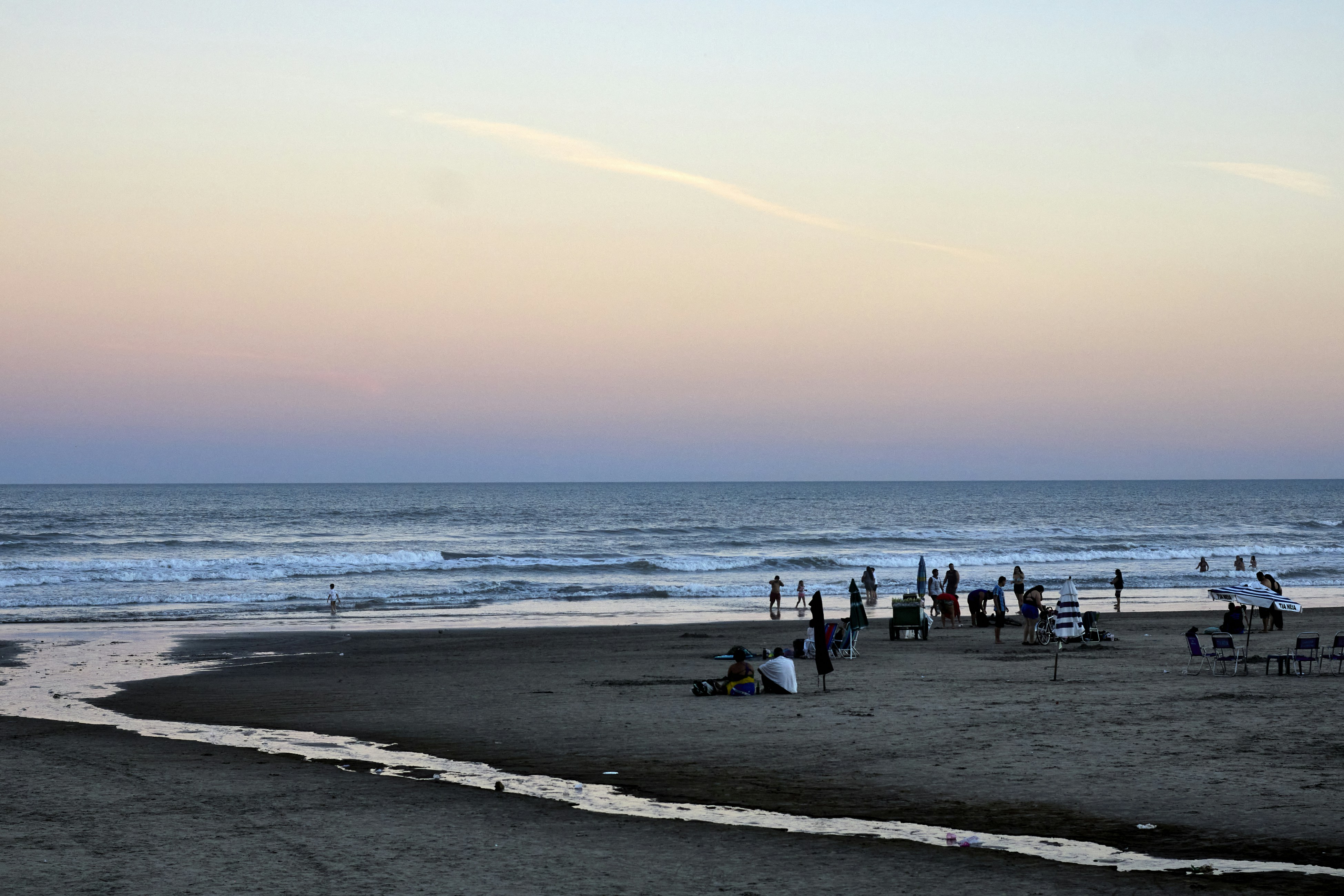 People on a sandy beach with a small stream under a soft sky.