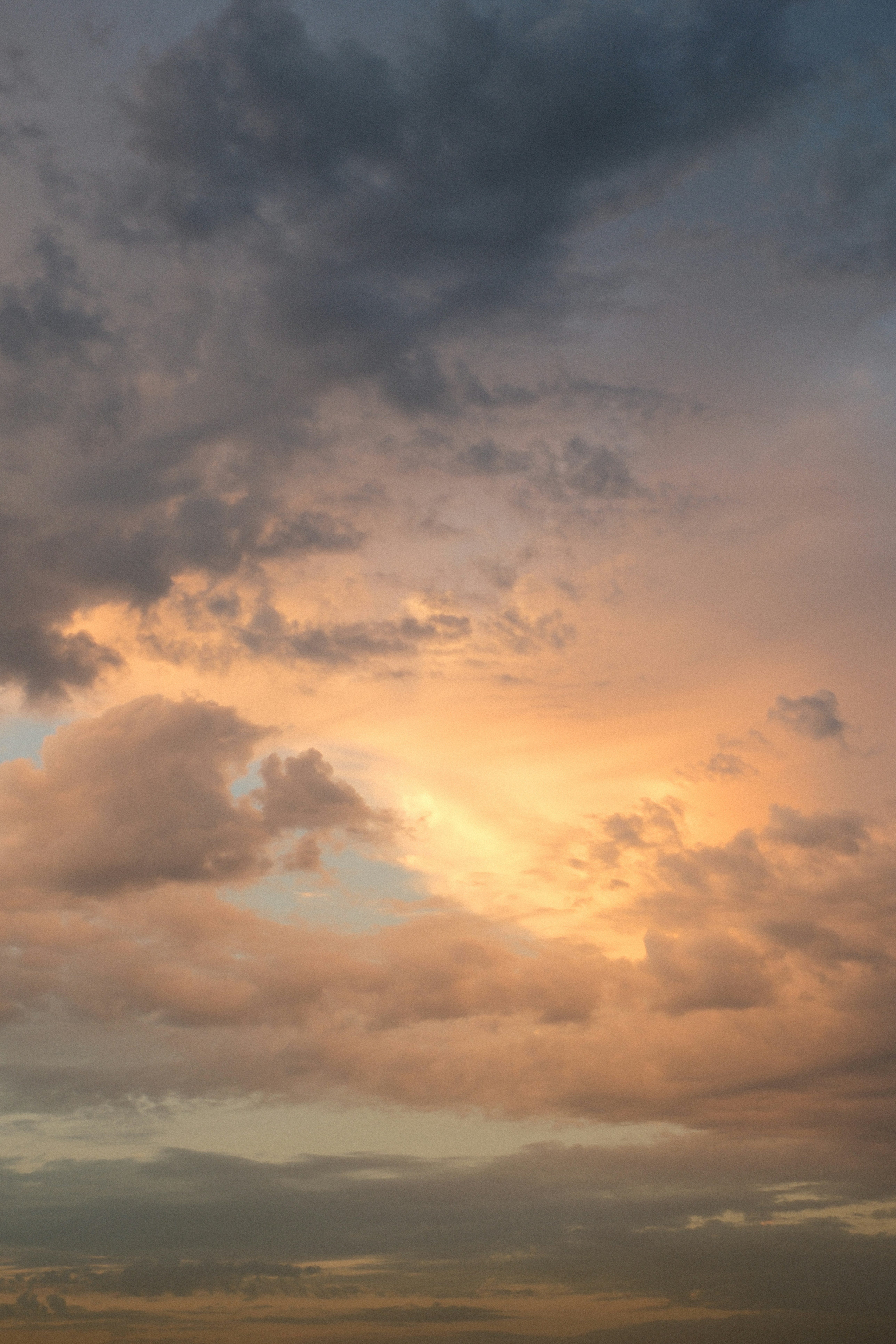 Soft sunset clouds glow with warm tones across a calm horizon, conveying quiet afterglow and atmospheric depth. This is a wide-angled sky scene, emphasizing color and light.