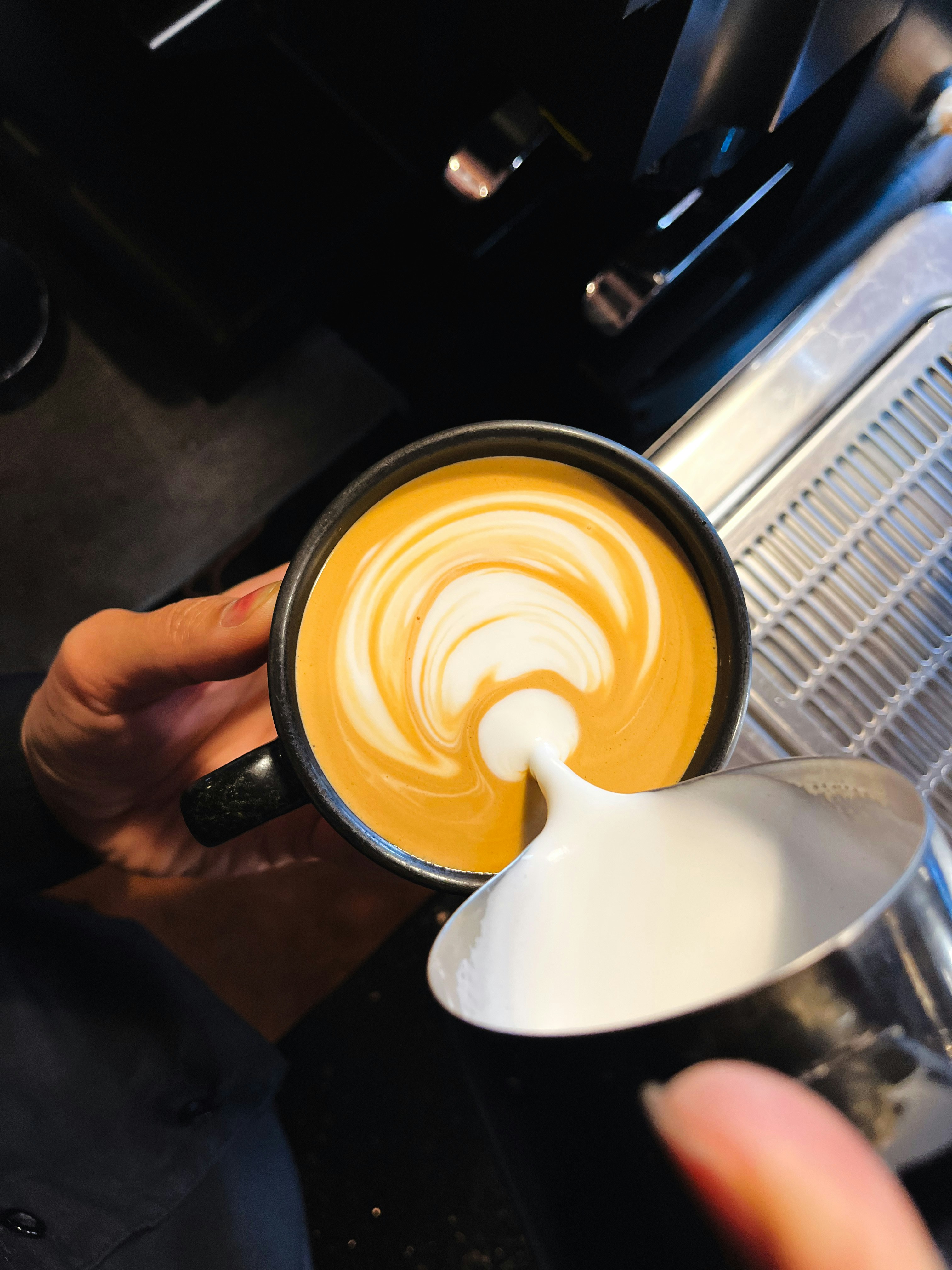 Swirled crema in a café cup as milk cascades from a stainless pitcher