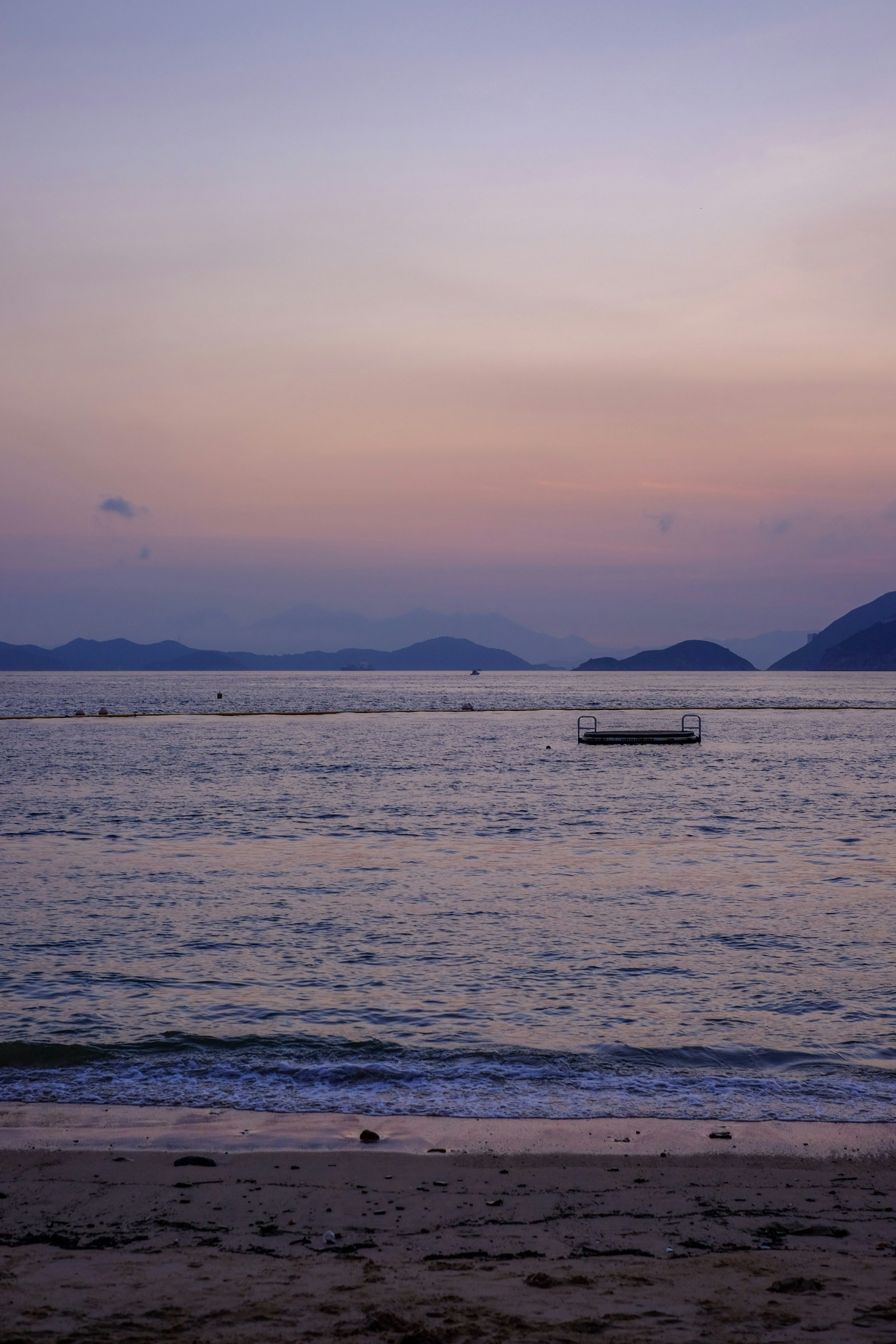 A floating platform on calm water with distant mountains under a soft purple sky.