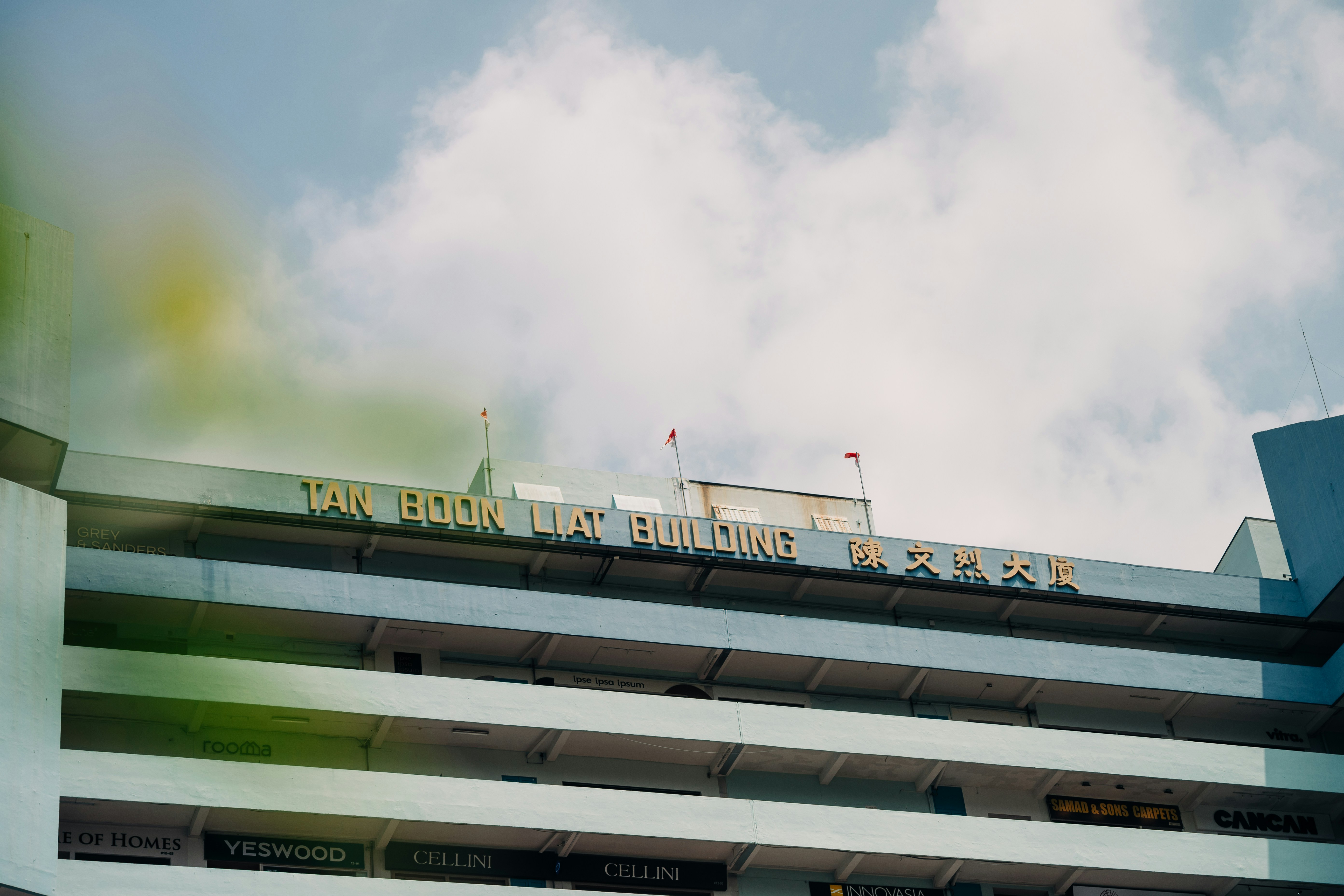Facade of a multi-storey building with signage in multiple languages under a bright, partly cloudy sky.