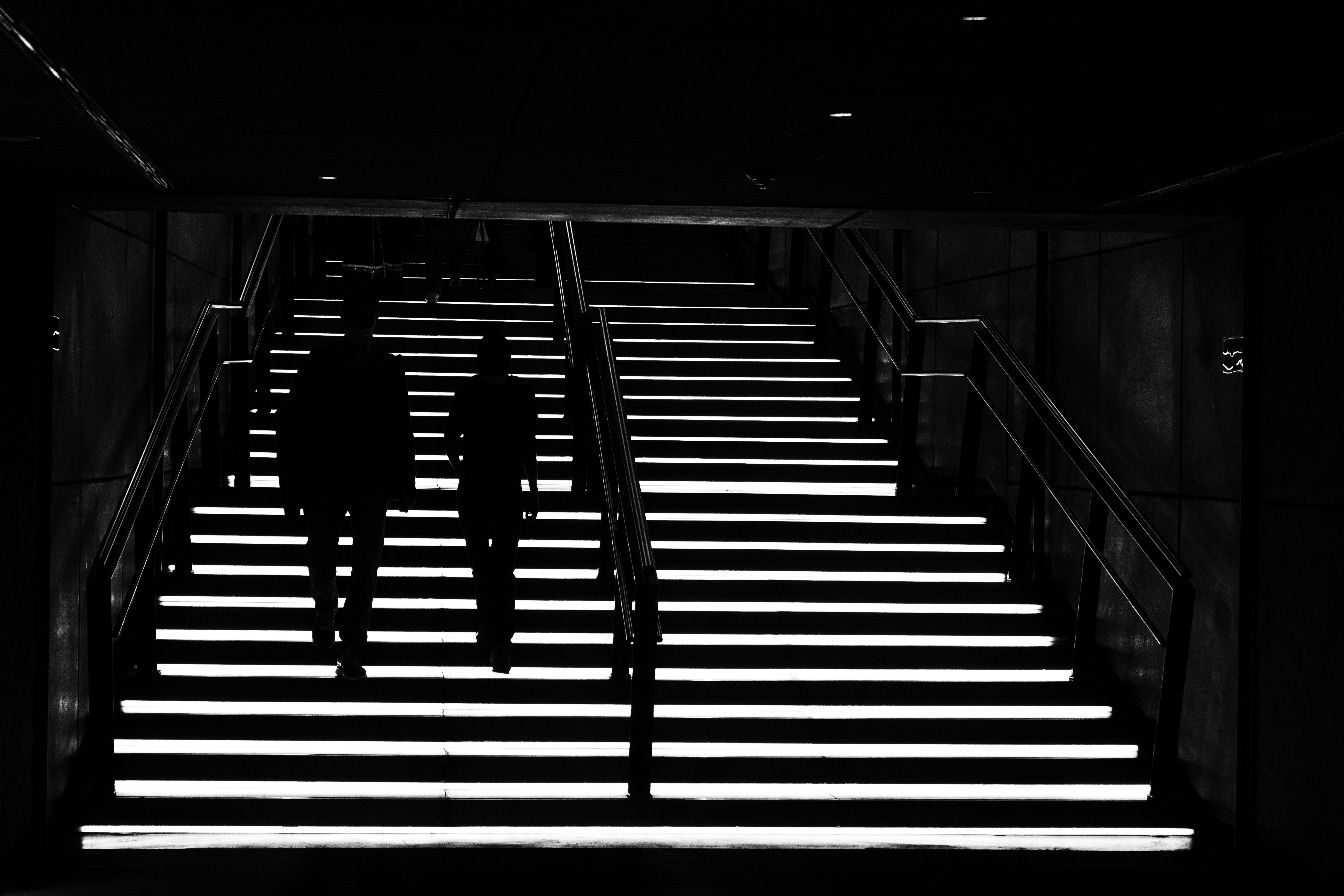 Shadowed Ascent: Two Figures Climb Neon-Outlined Stairs